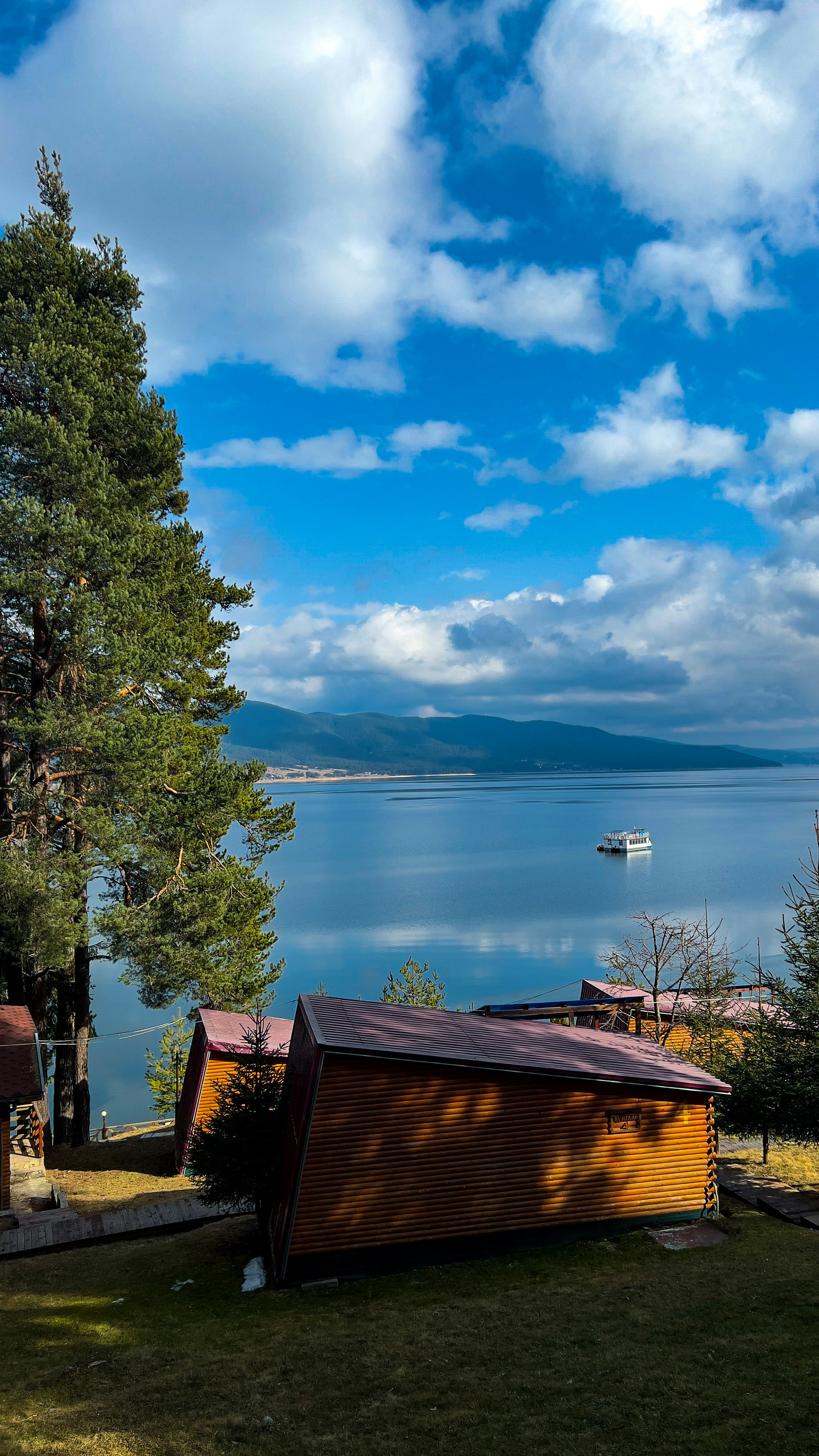 Lakeside Outpost: Pines, Cabins, and a Quiet Boat on Calm Blue Waters