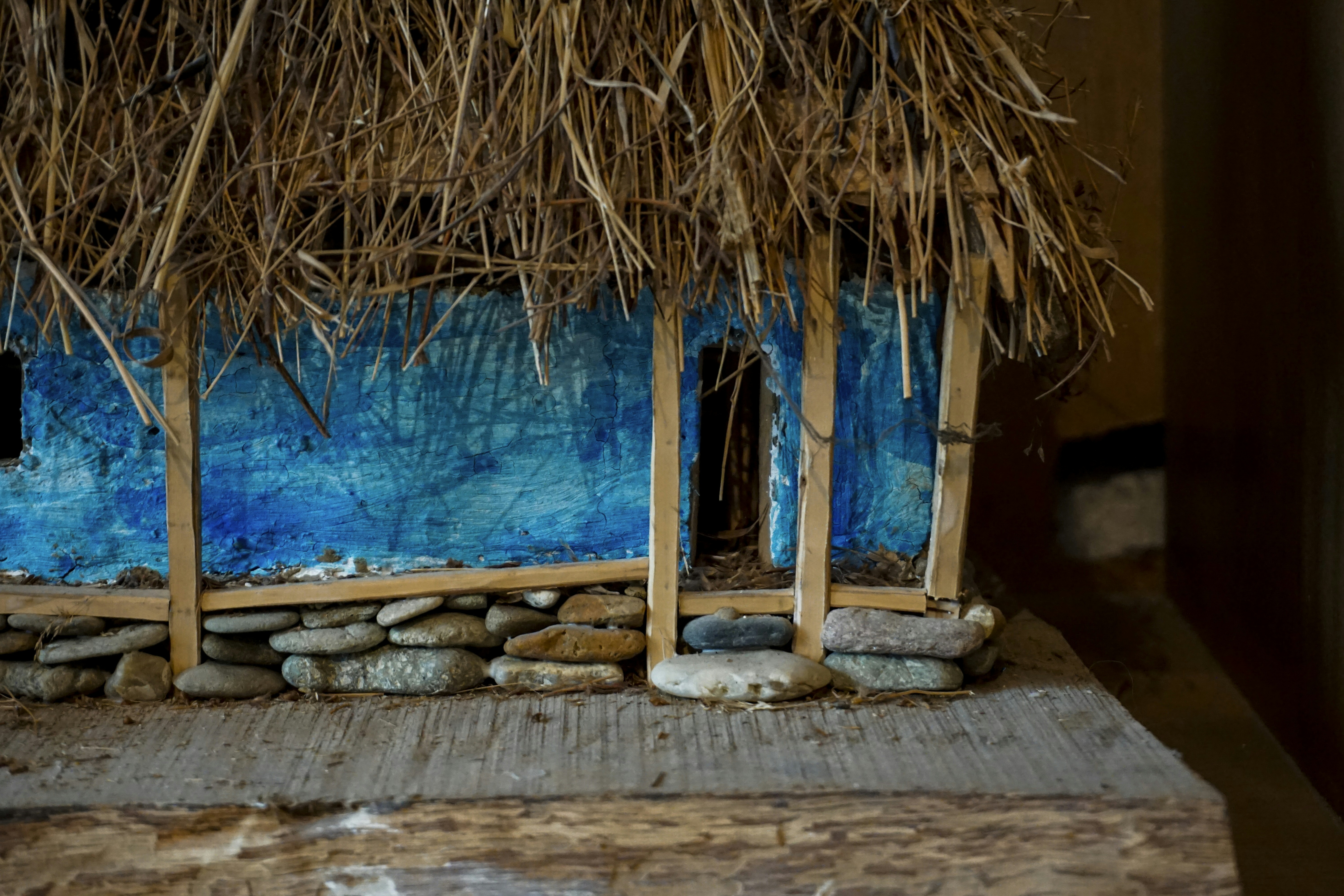 Thatched Micro-Hut on a Stone Plinth Against a Turquoise Backdrop