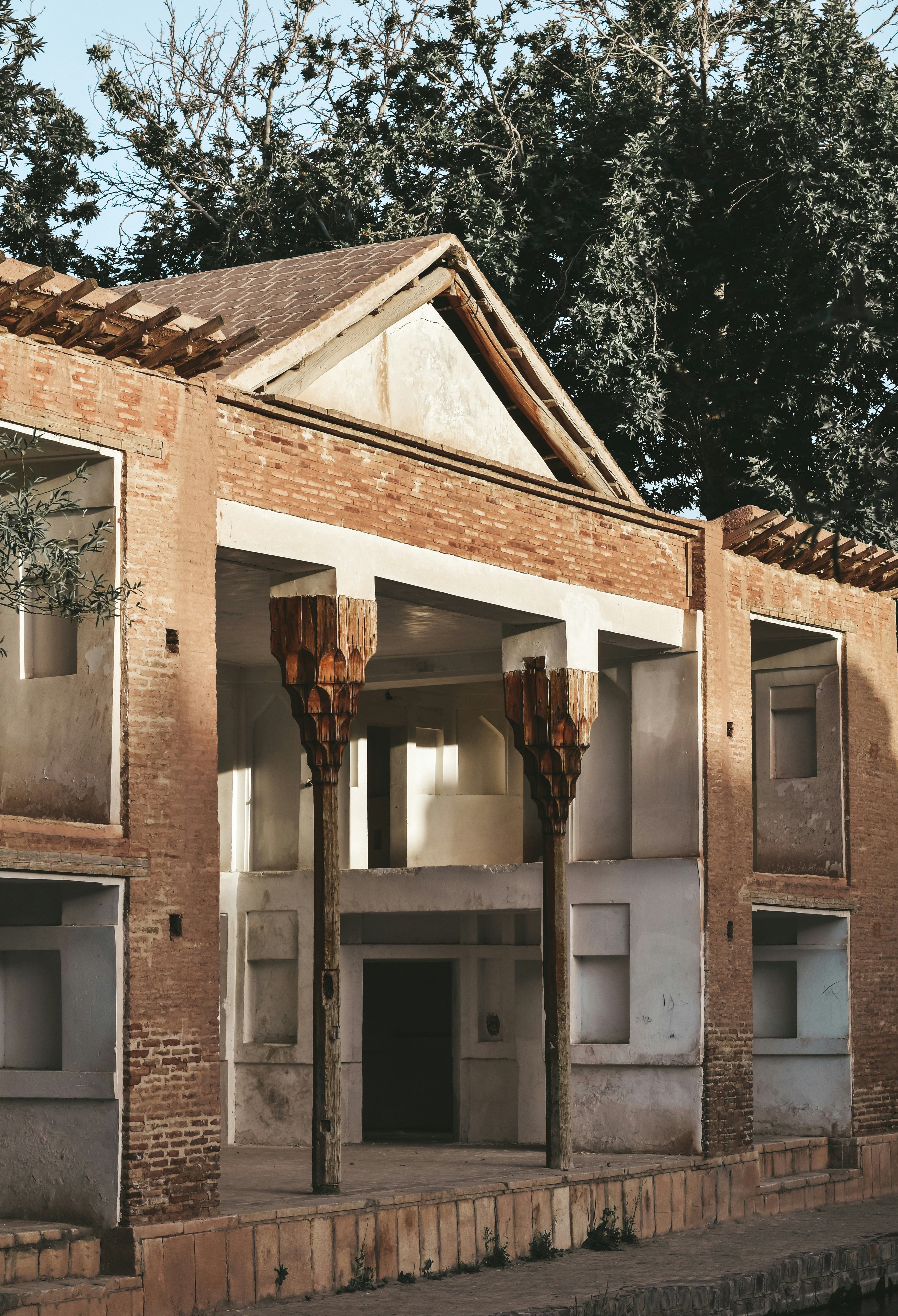 A rustic building with brick and wood elements, surrounded by trees in soft morning light.