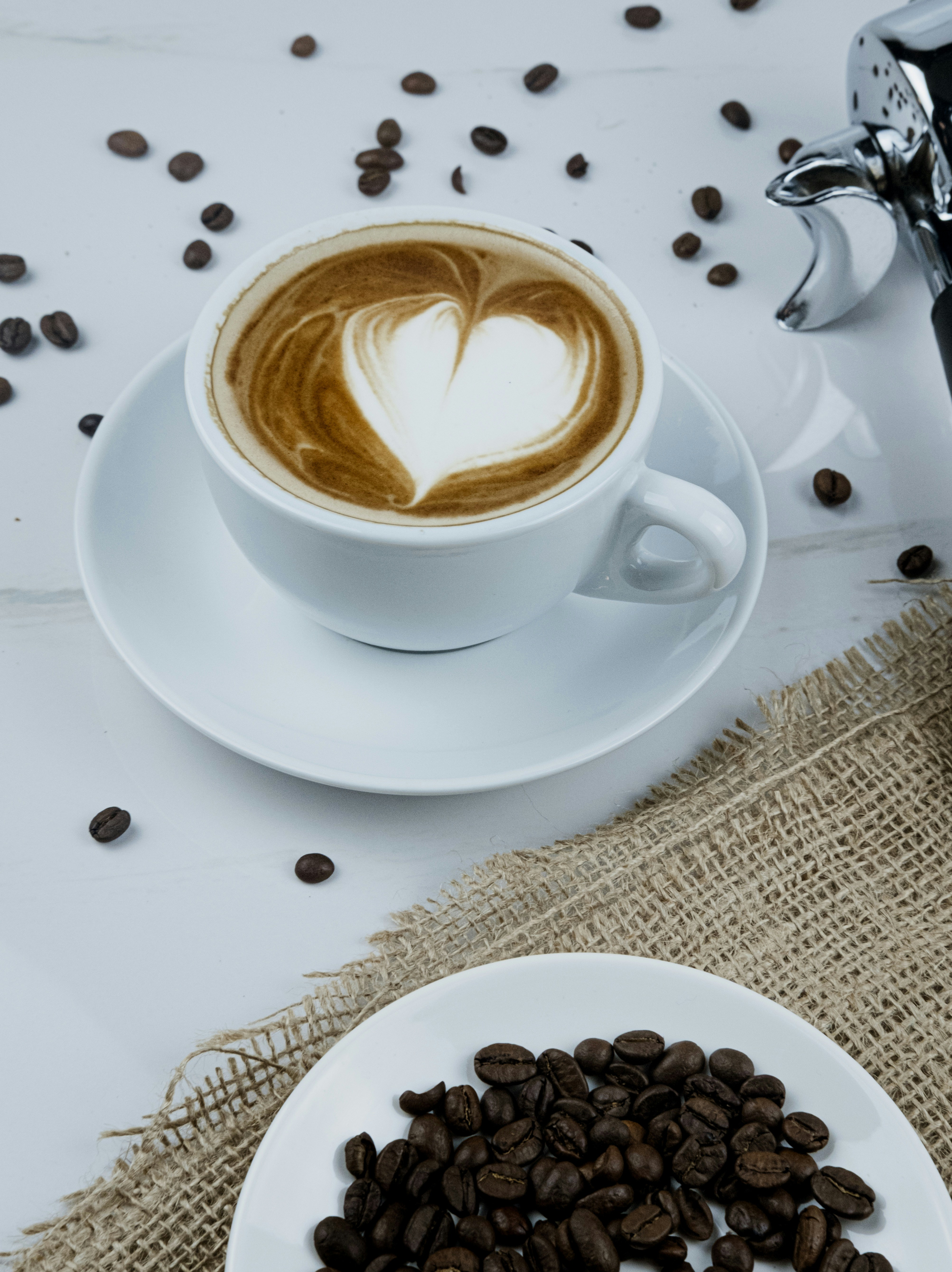 A white plate topped with a heart shaped latte next to a cup of coffee ...