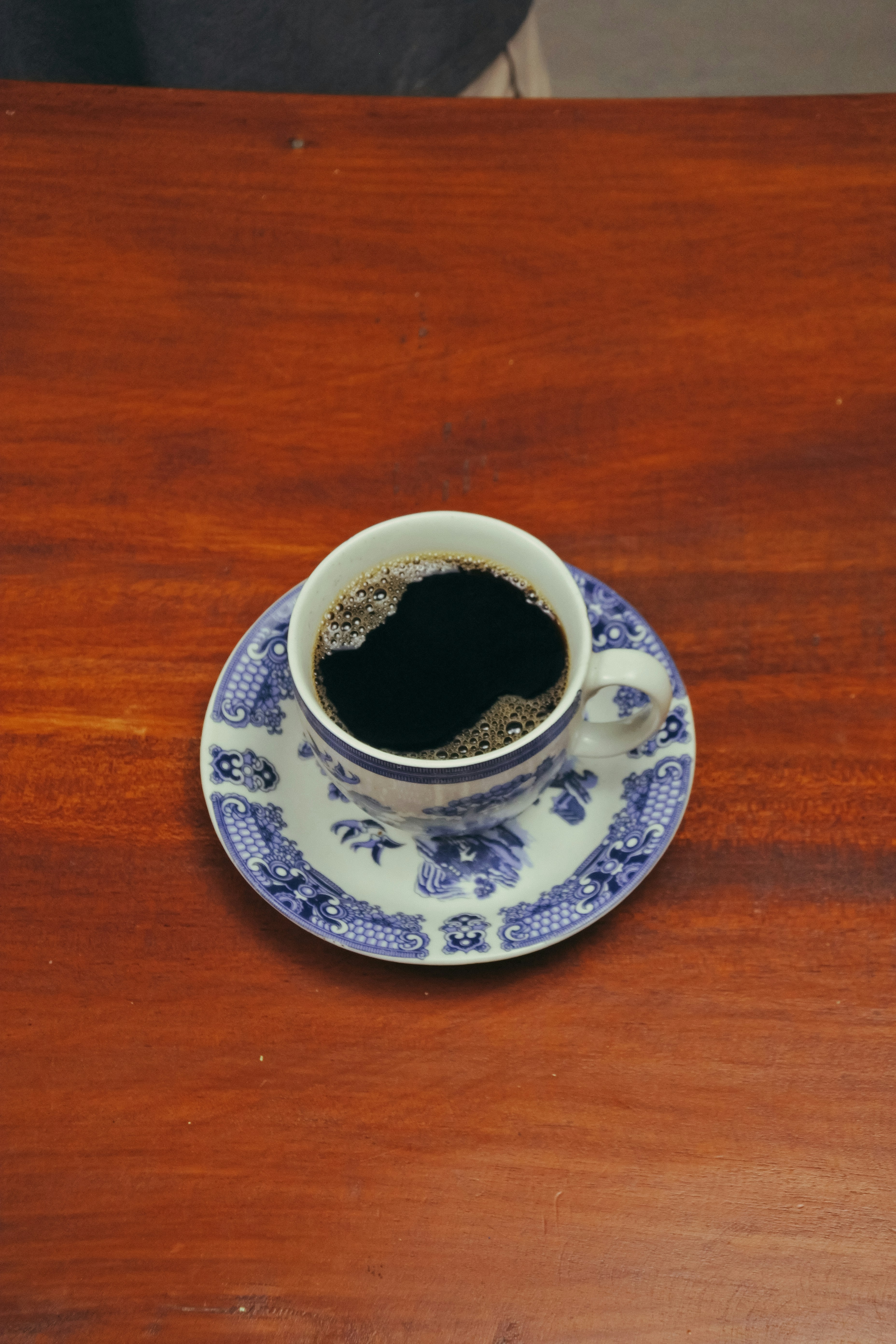 Black coffee served in an intricately designed porcelain cup on a polished wooden table.