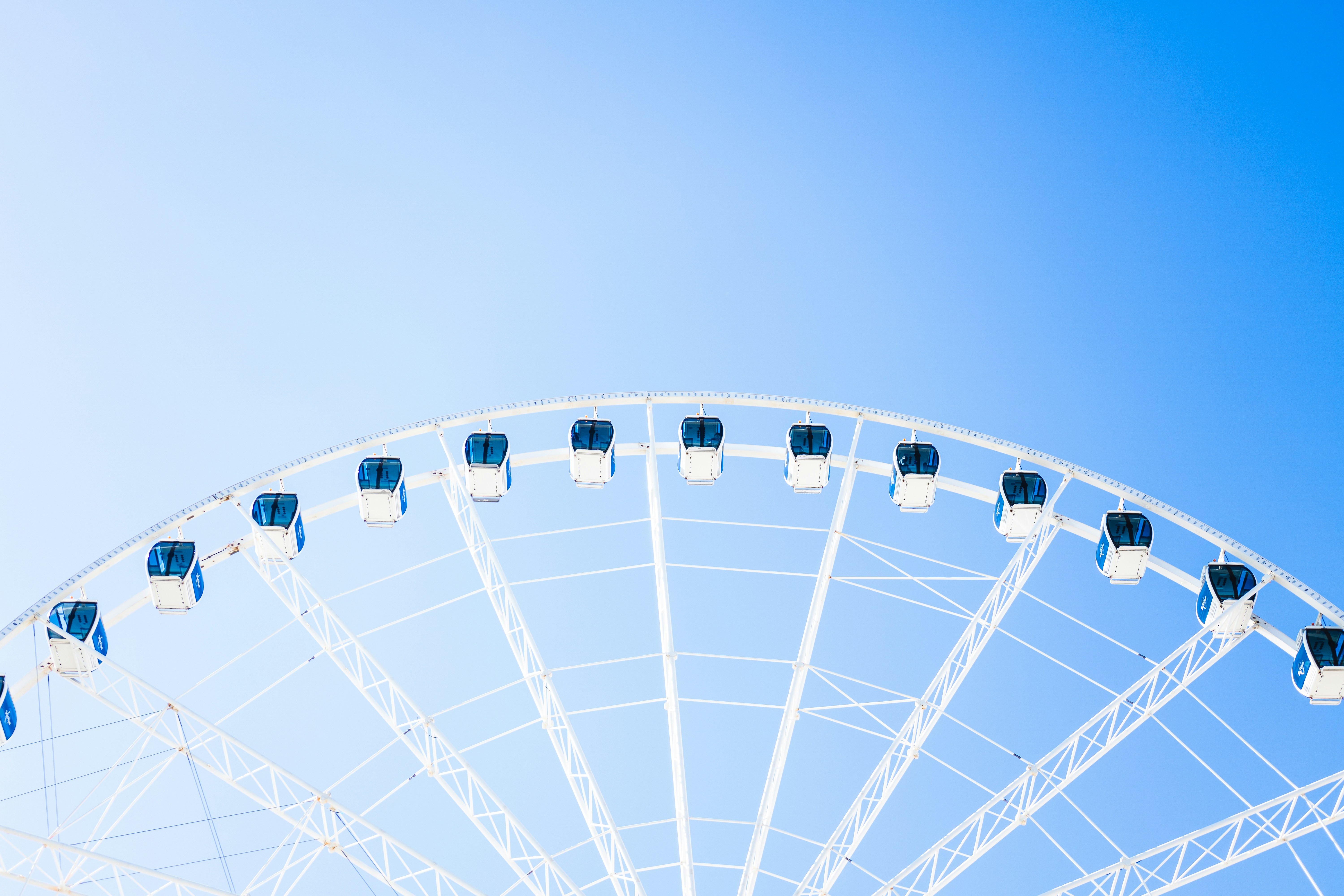 Ferris wheel's white frame and gondolas curve along the lower edge of a pale blue sky.