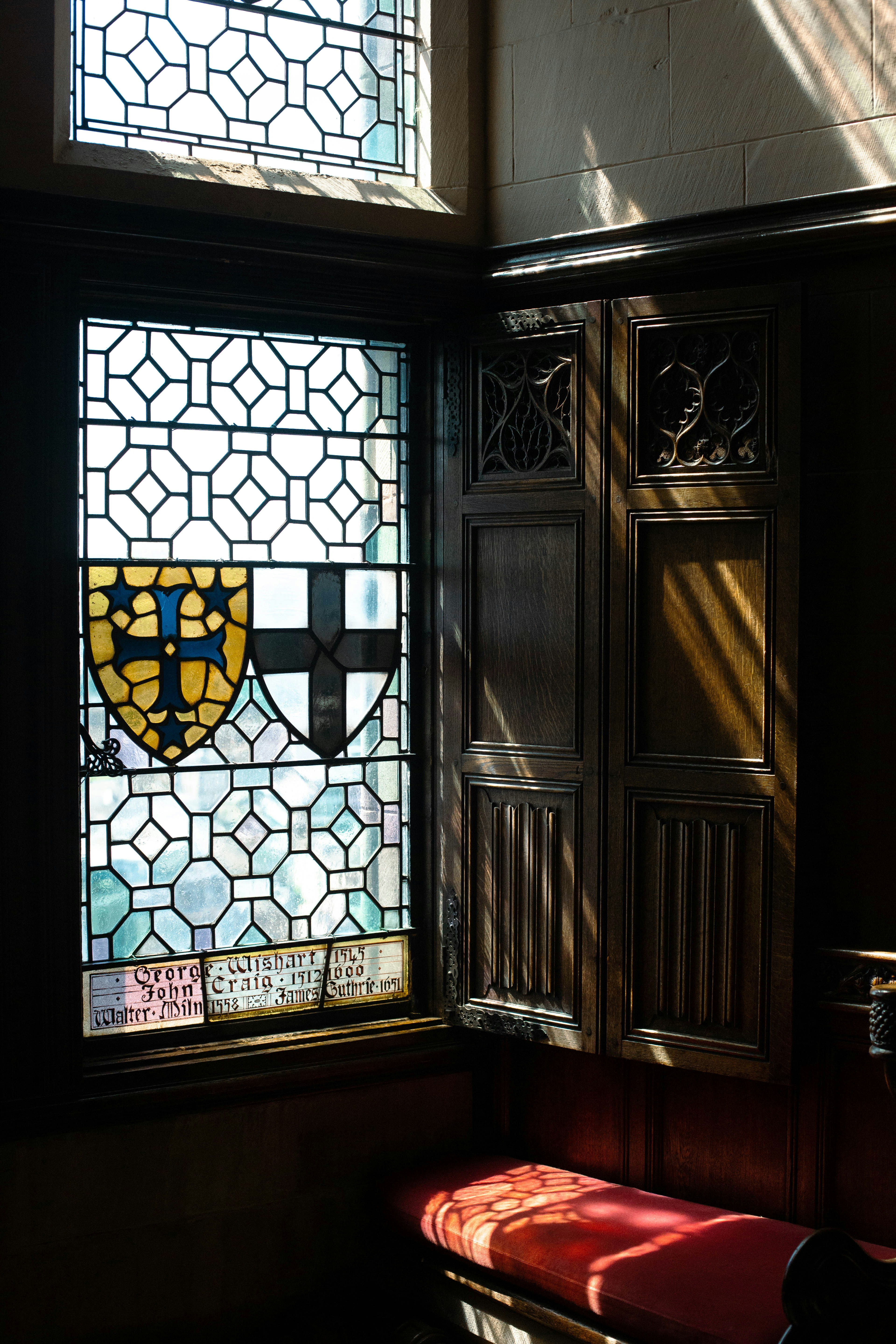 Heraldic Glass and Warm Wood: Light on a Red-Cushioned Bench