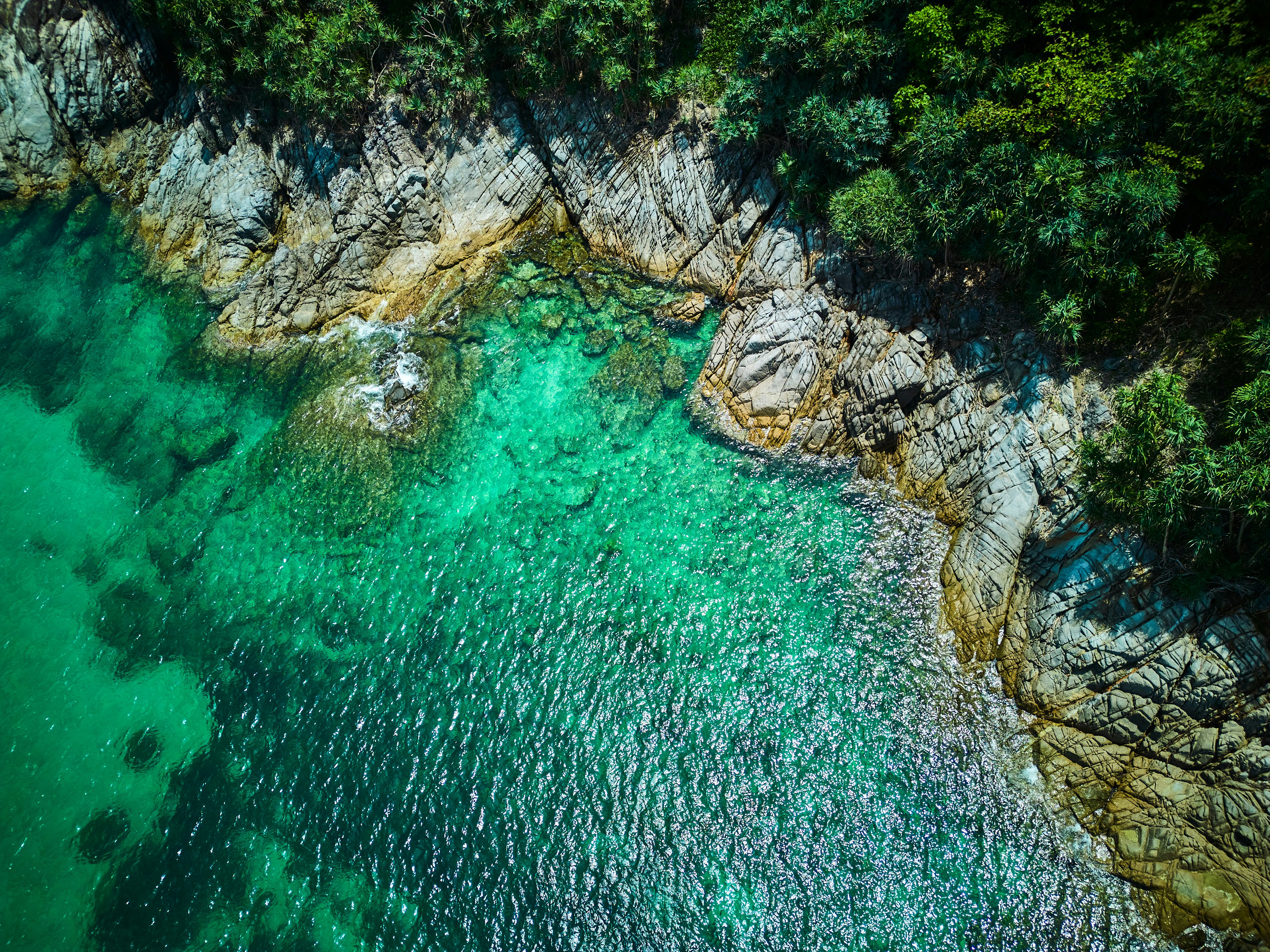 Aerial view of rugged coastline with turquoise waters and lush greenery.
