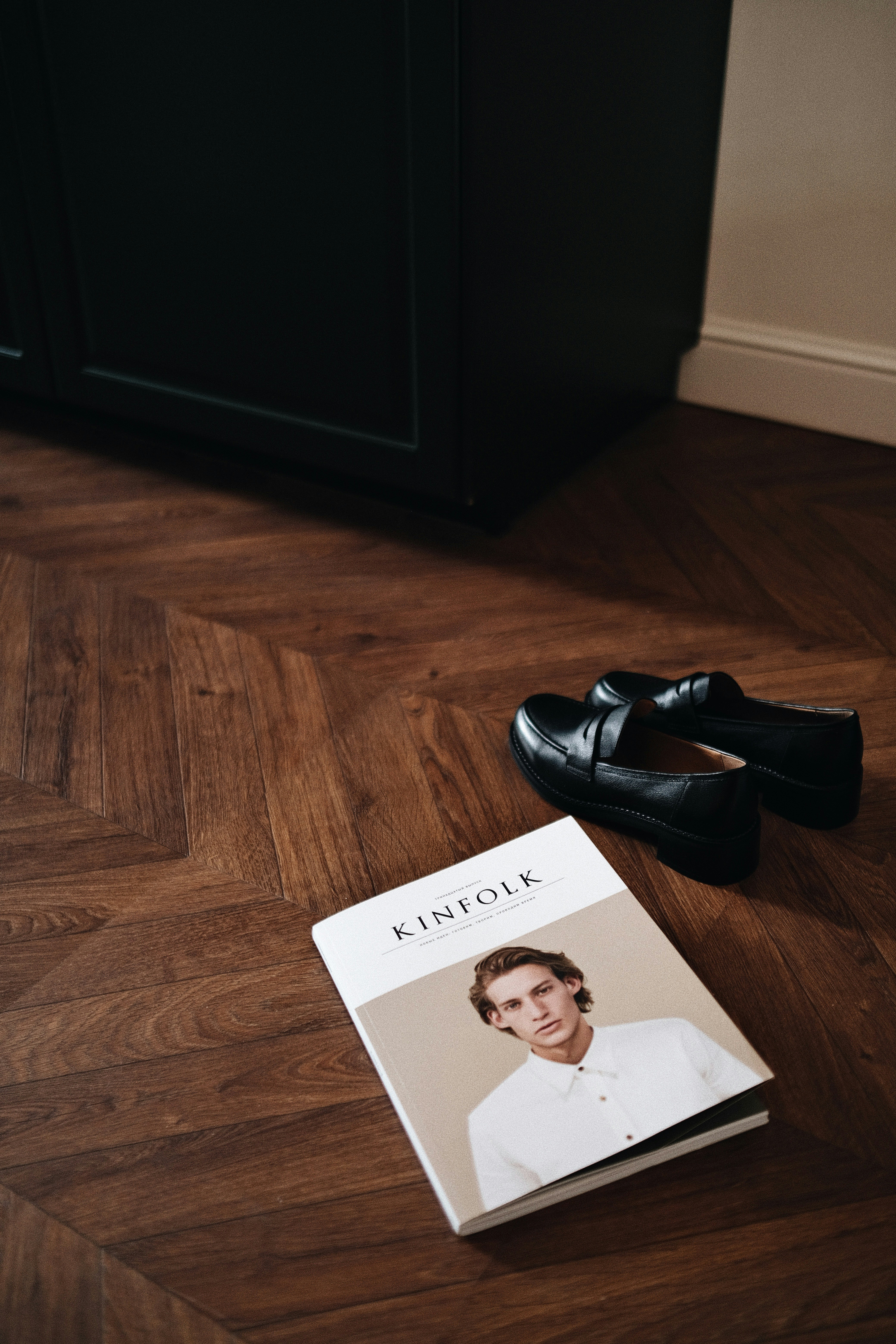 KINFOLK magazine resting on polished wooden floor with stylish black shoes nearby.