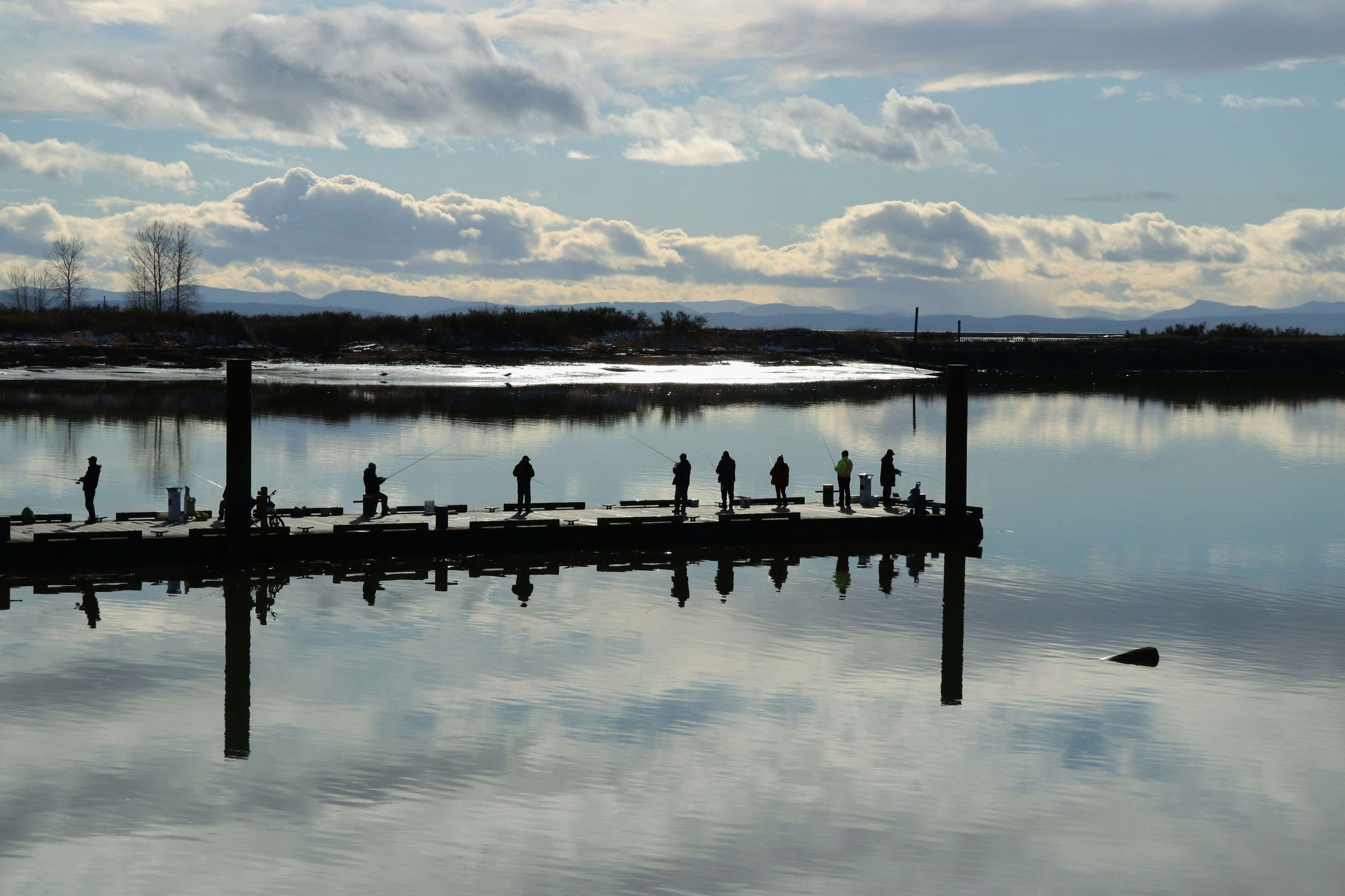 People lined along a dock over still water under a cloudy winter sky.