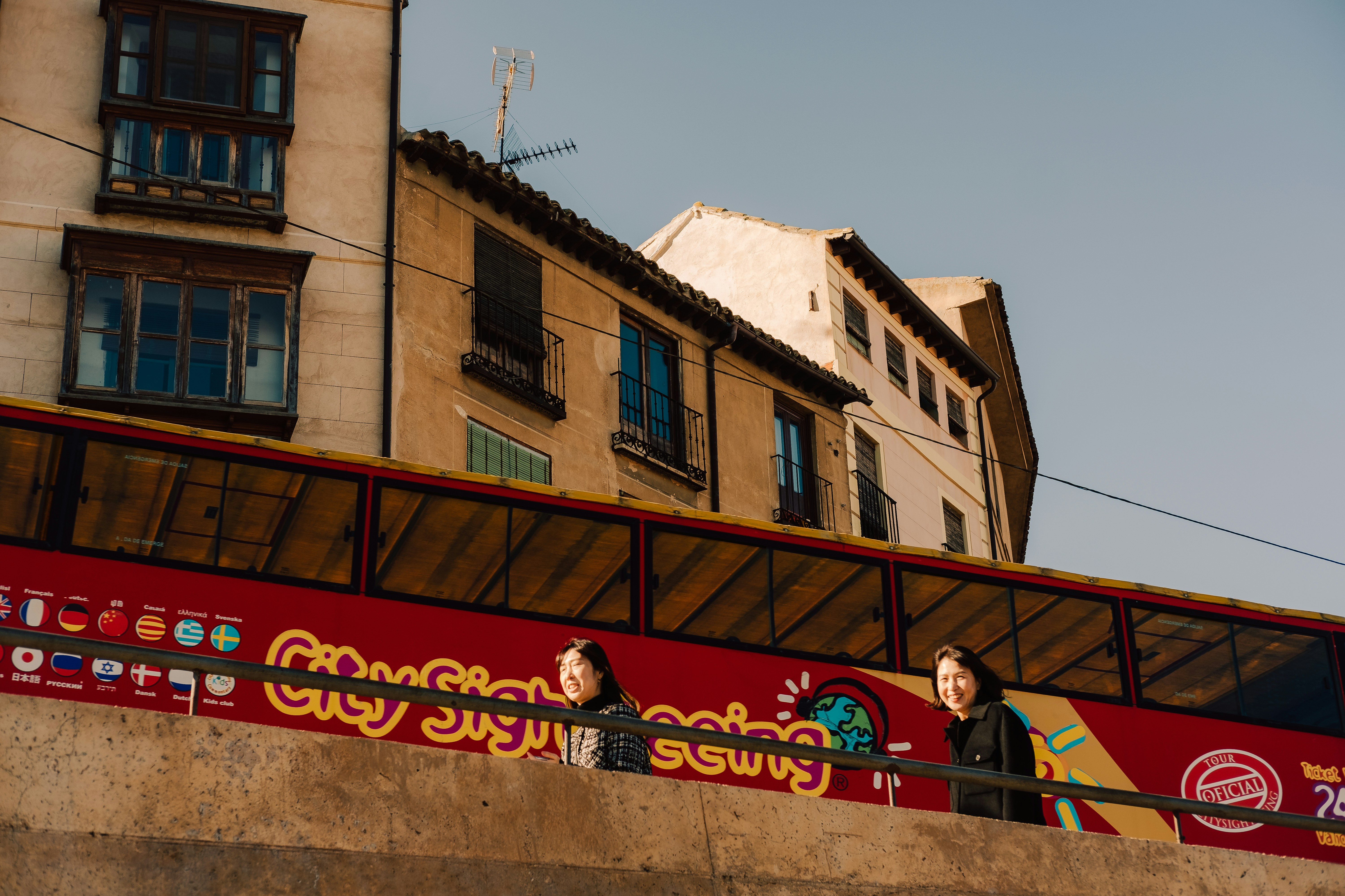 Two people stand on a bridge adorned with colorful graffiti, with historic buildings in the background.