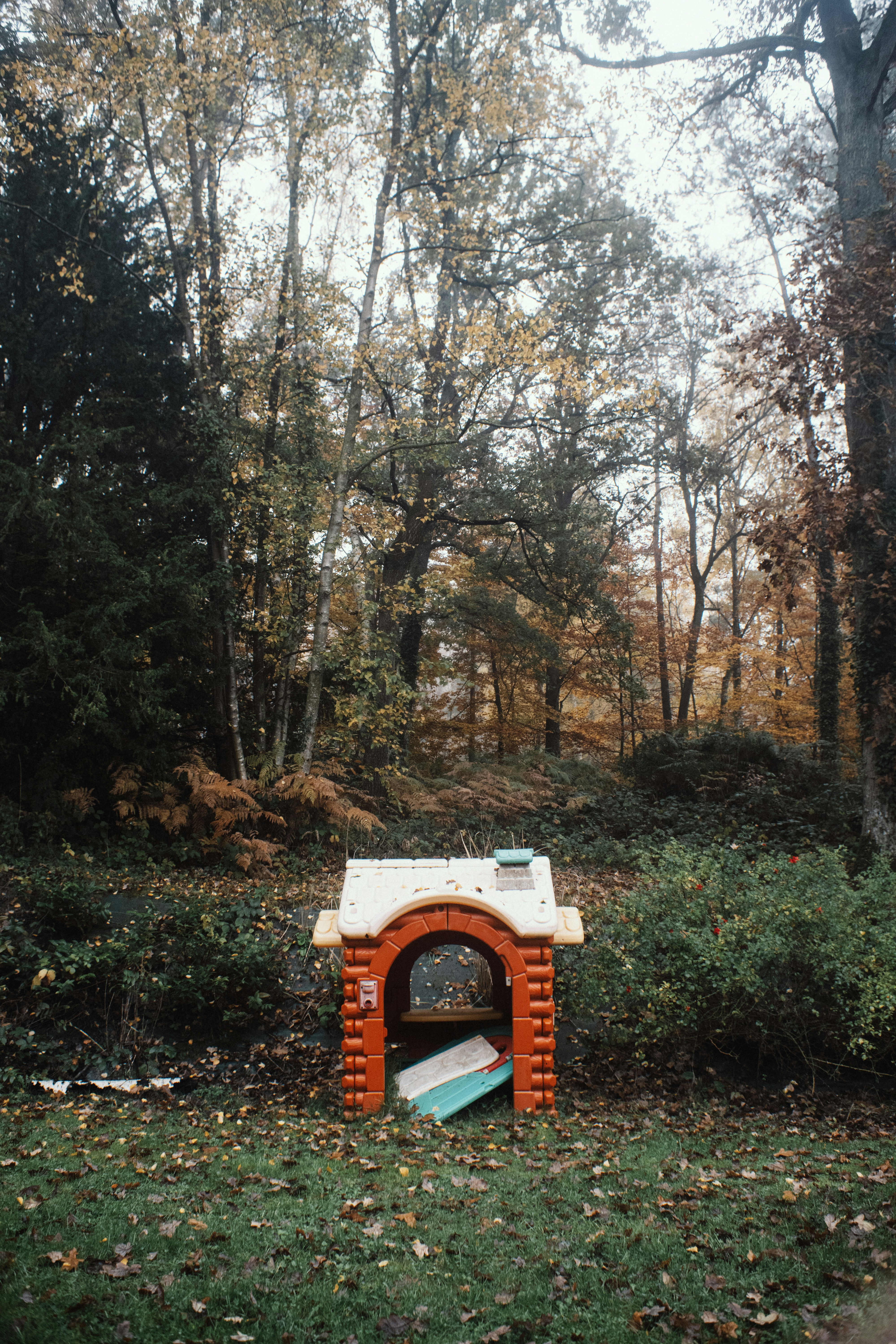 Colorful plastic playhouse nestled in a serene autumn landscape, surrounded by fallen leaves and trees. The scene evokes nostalgia and the quiet beauty of childhood adventures.