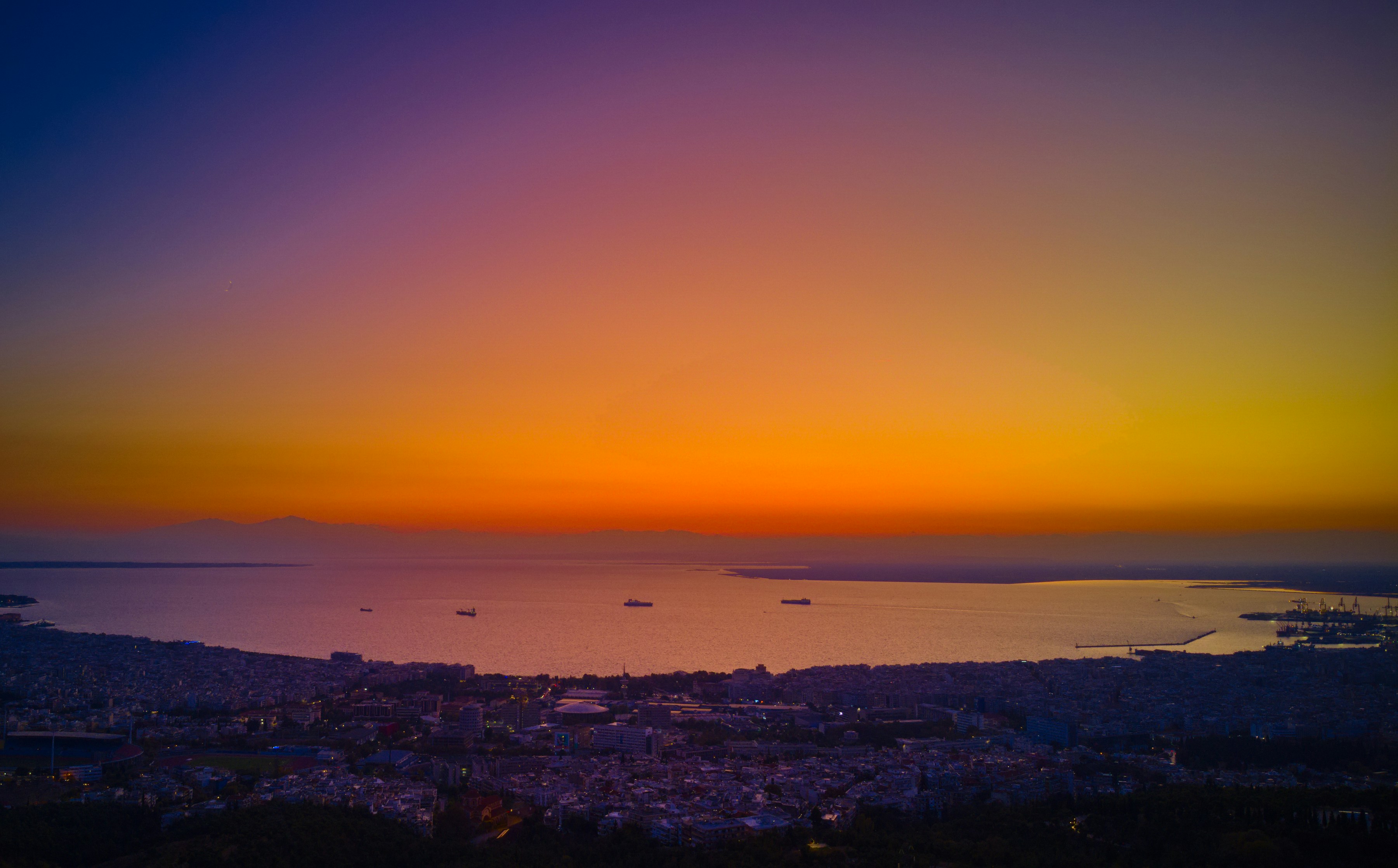 Thessaloniki cityscape under a vibrant sunset, with orange and purple hues reflecting on the Thermaic Gulf.