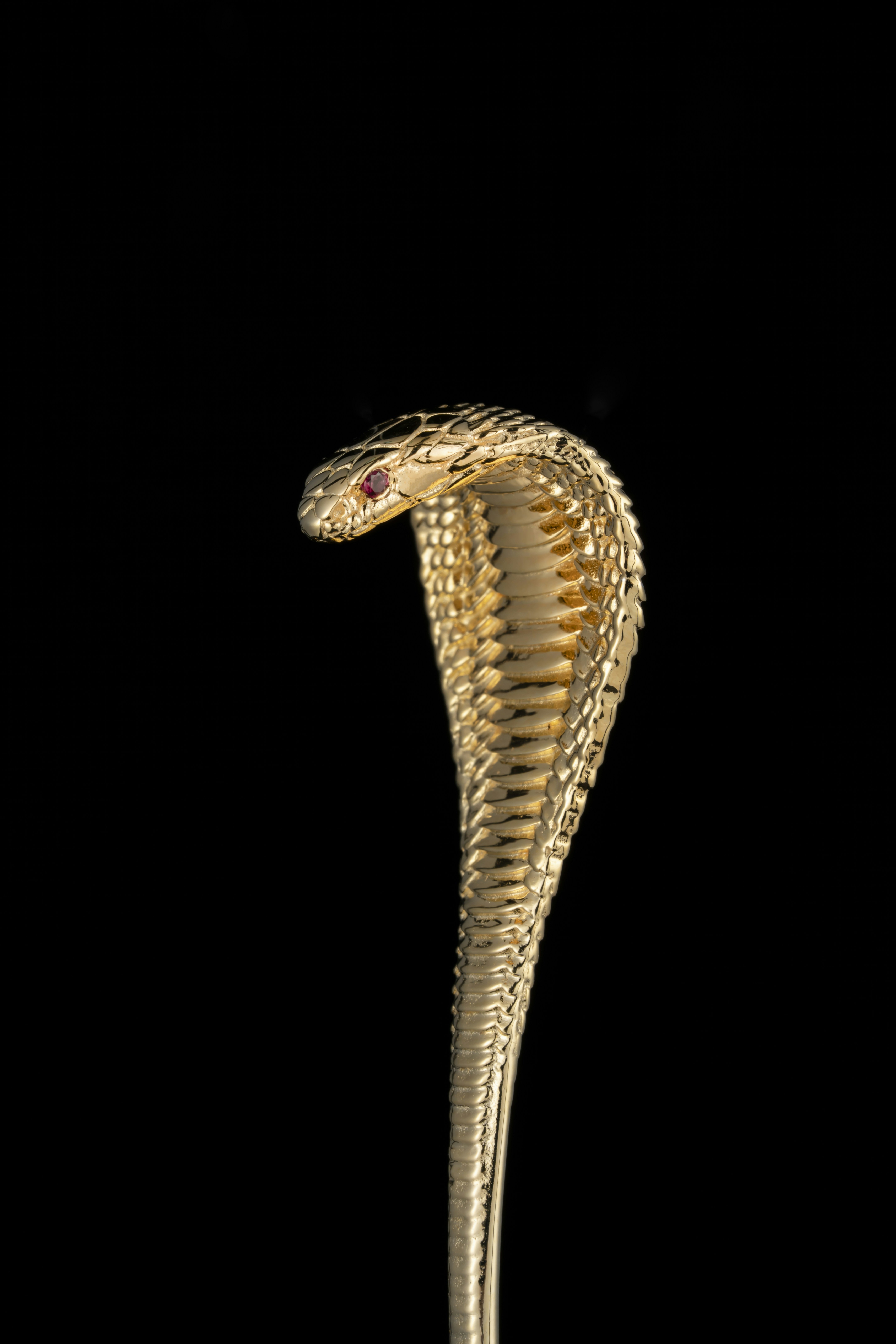 Intricately designed golden snake sculpture with ruby eyes, set against a black background.