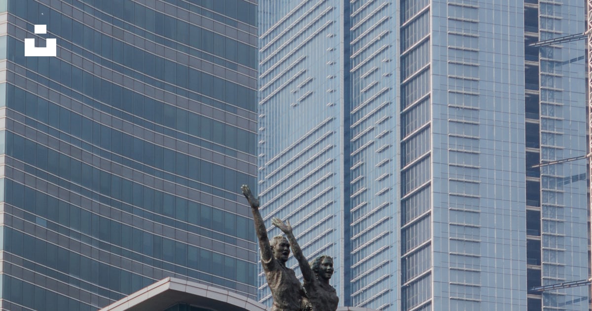 Foto Una Estatua De Dos Hombres En Un Pedestal Frente A Edificios Altos