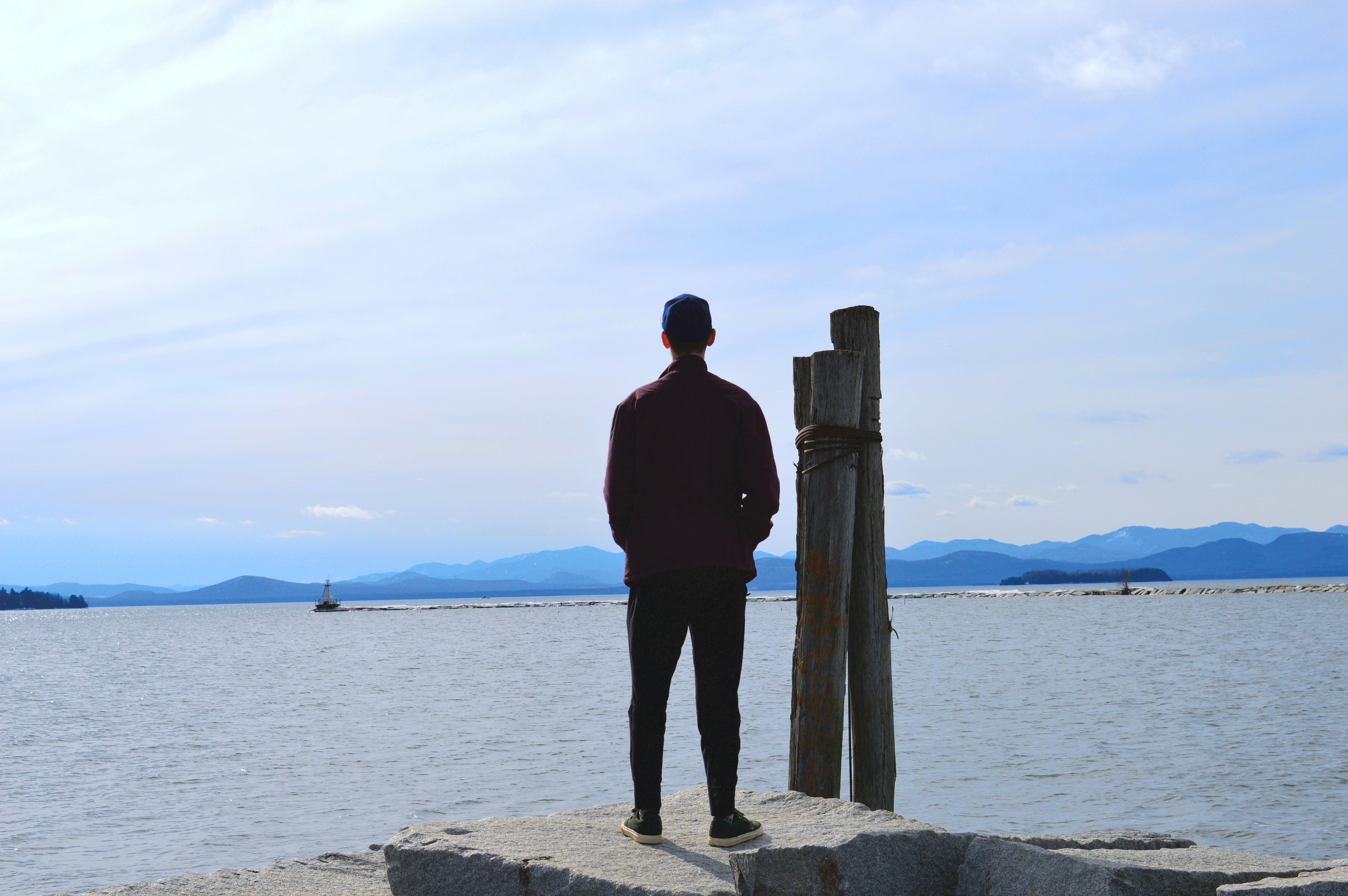 Silhouette of a person standing on a pier overlooking a calm lake with mountains in the distance.