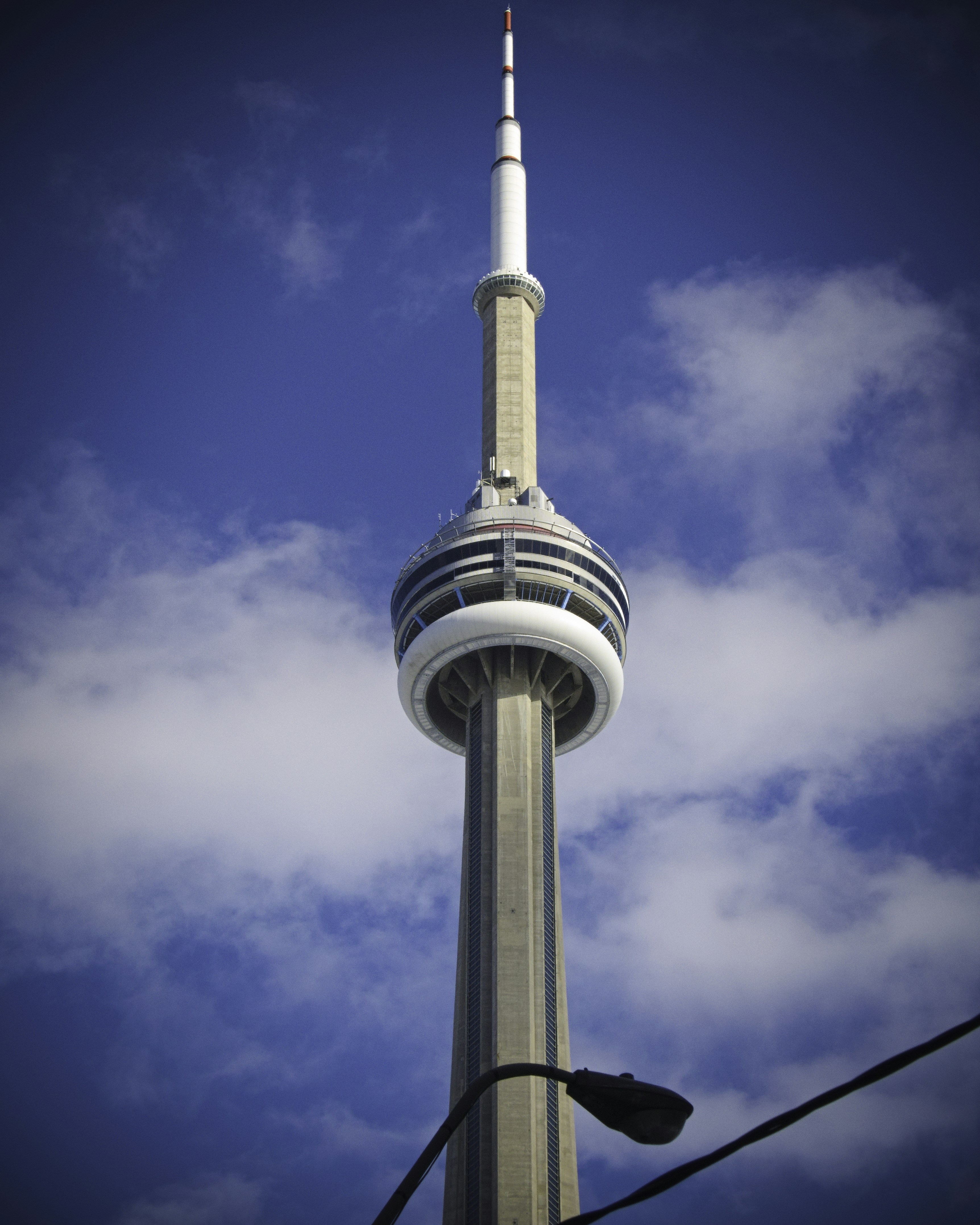 Iconic CN Tower piercing the sky, surrounded by fluffy clouds and a hint of urban infrastructure below.