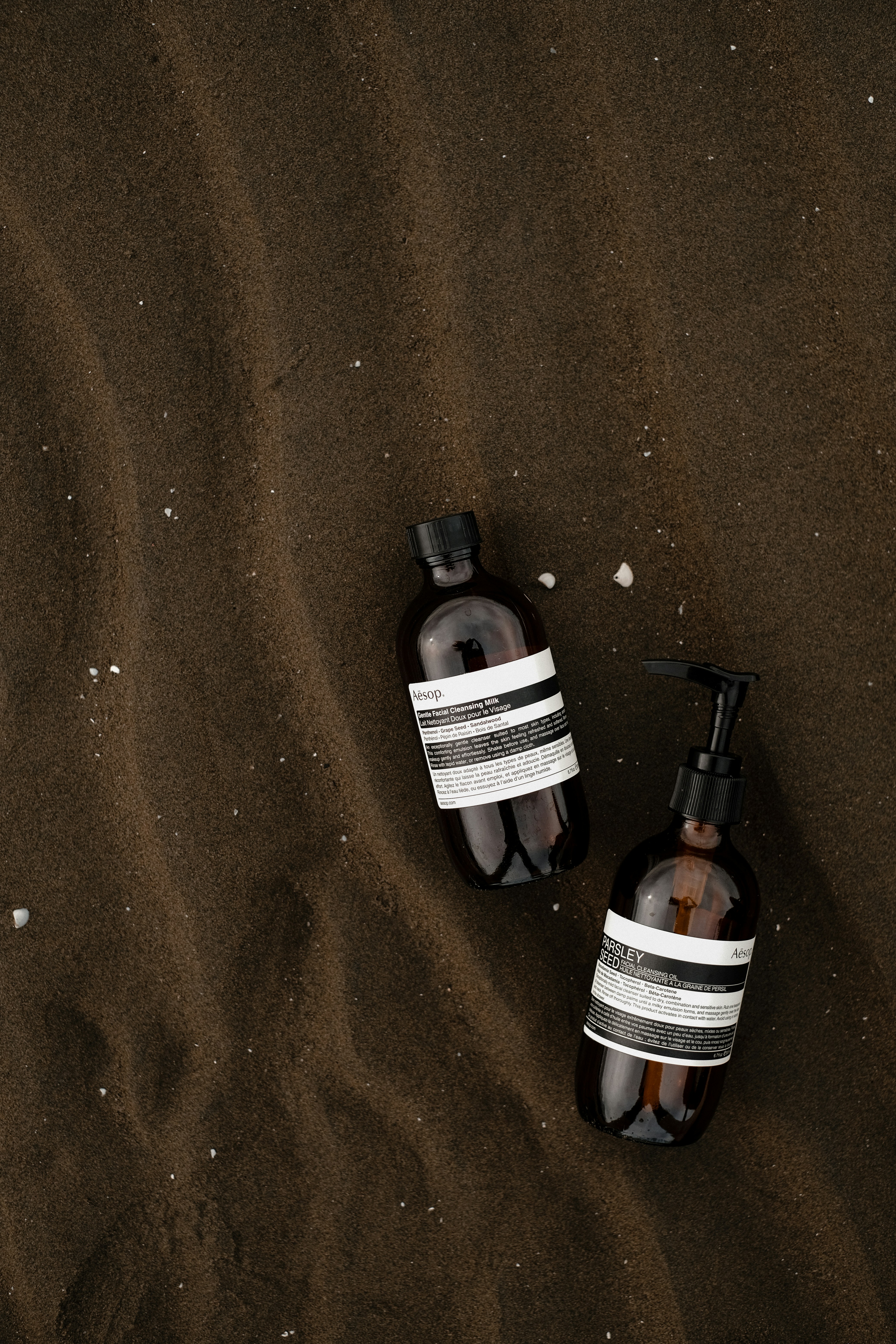 Two amber bottles resting in wind-sculpted beach sand