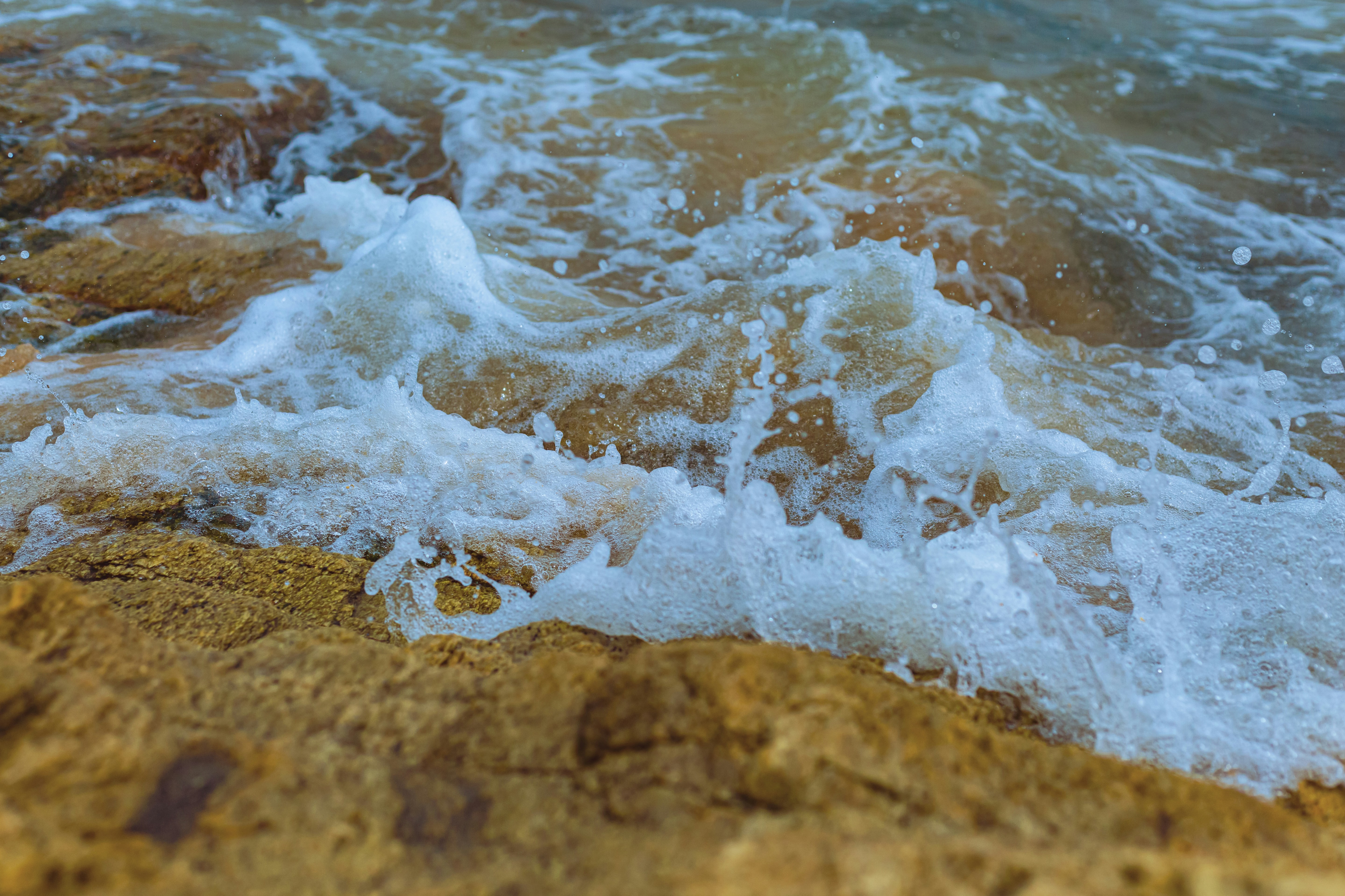 Foamy waves crashing against textured rocks on a vibrant shoreline.