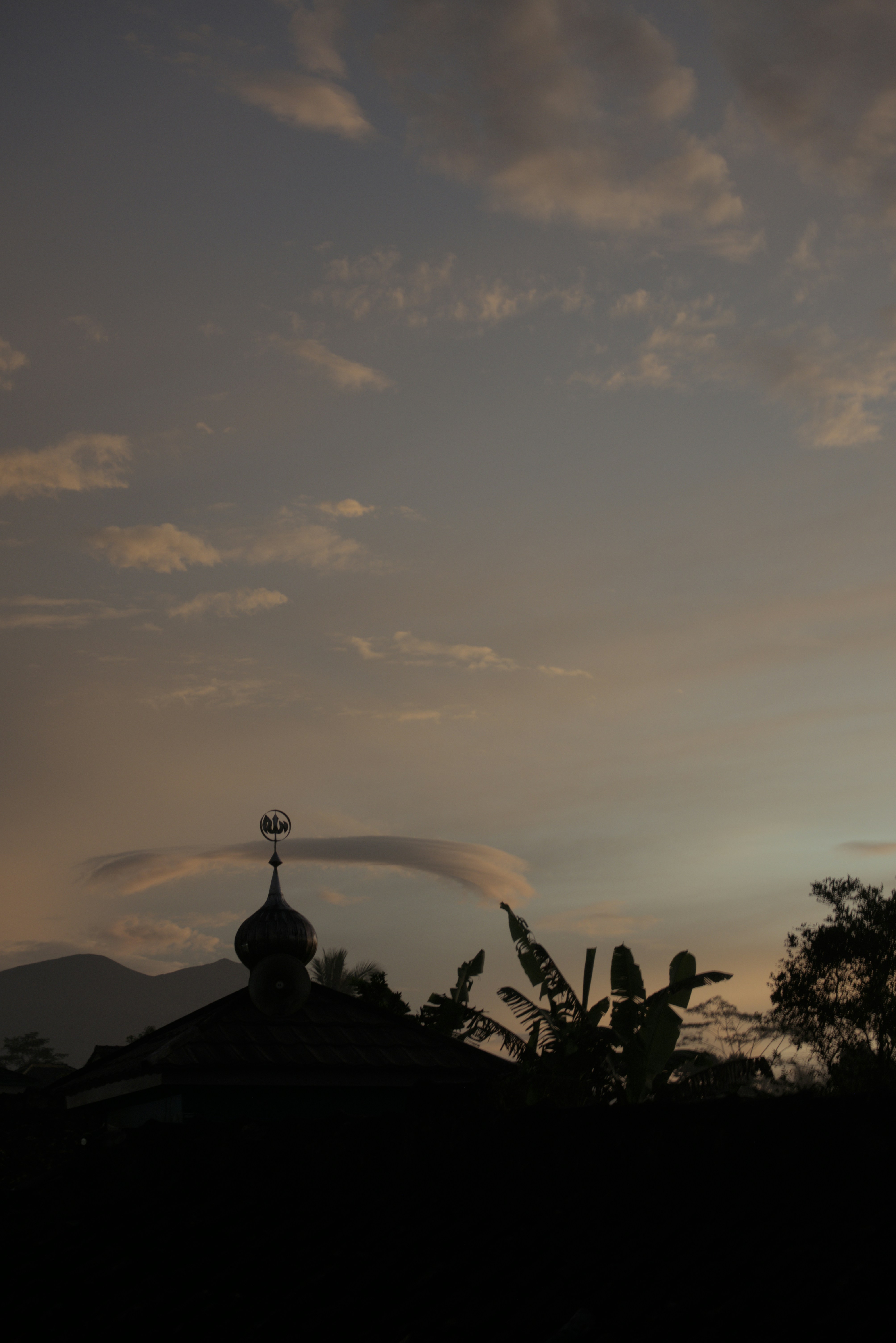 Silhouette of a mosque with Mount Gede in the background under a dawn sky.