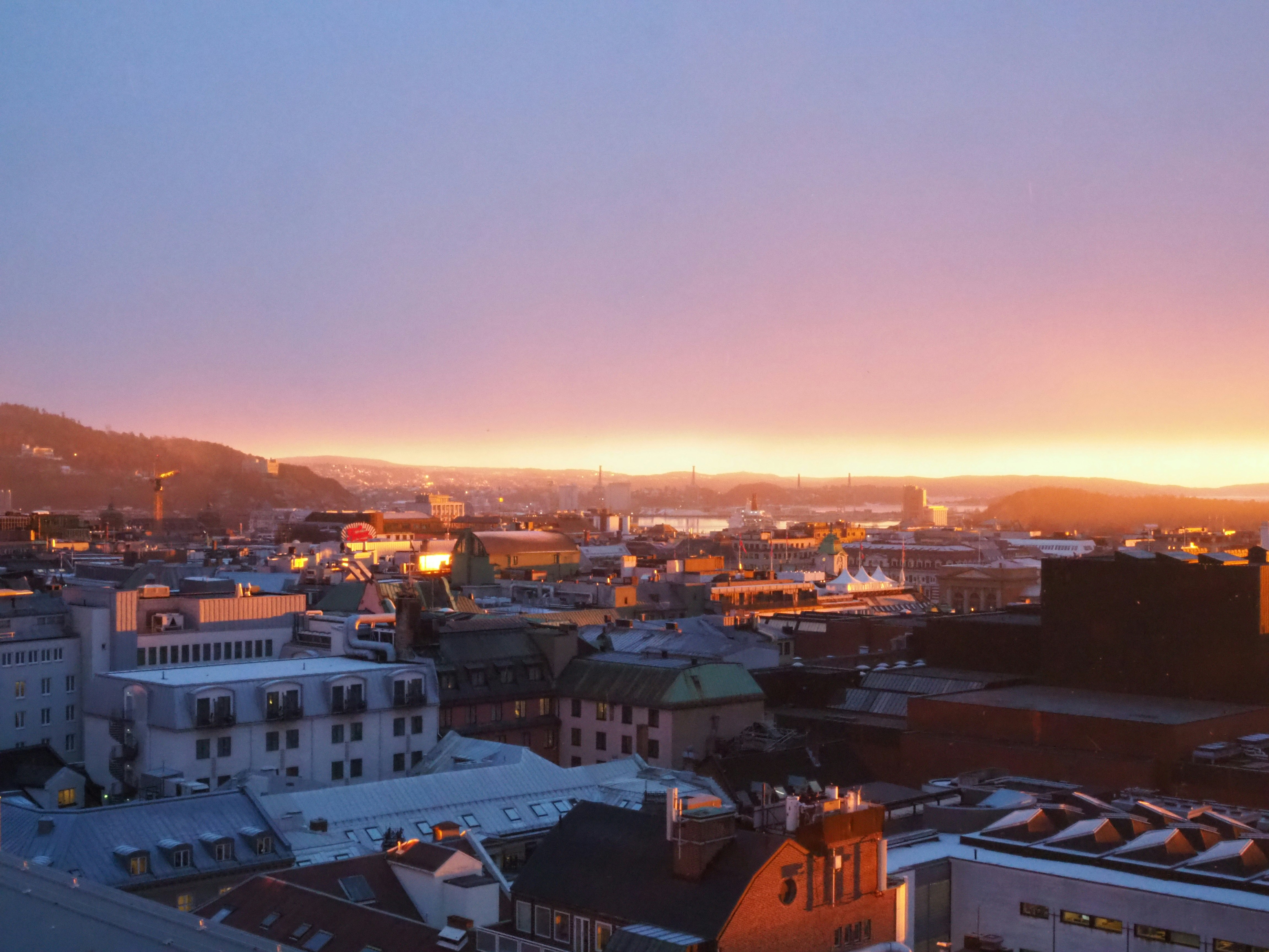 Vibrant sunset casting golden hues over a city skyline, highlighting rooftops and distant hills. The scene captures the transition from day to night.