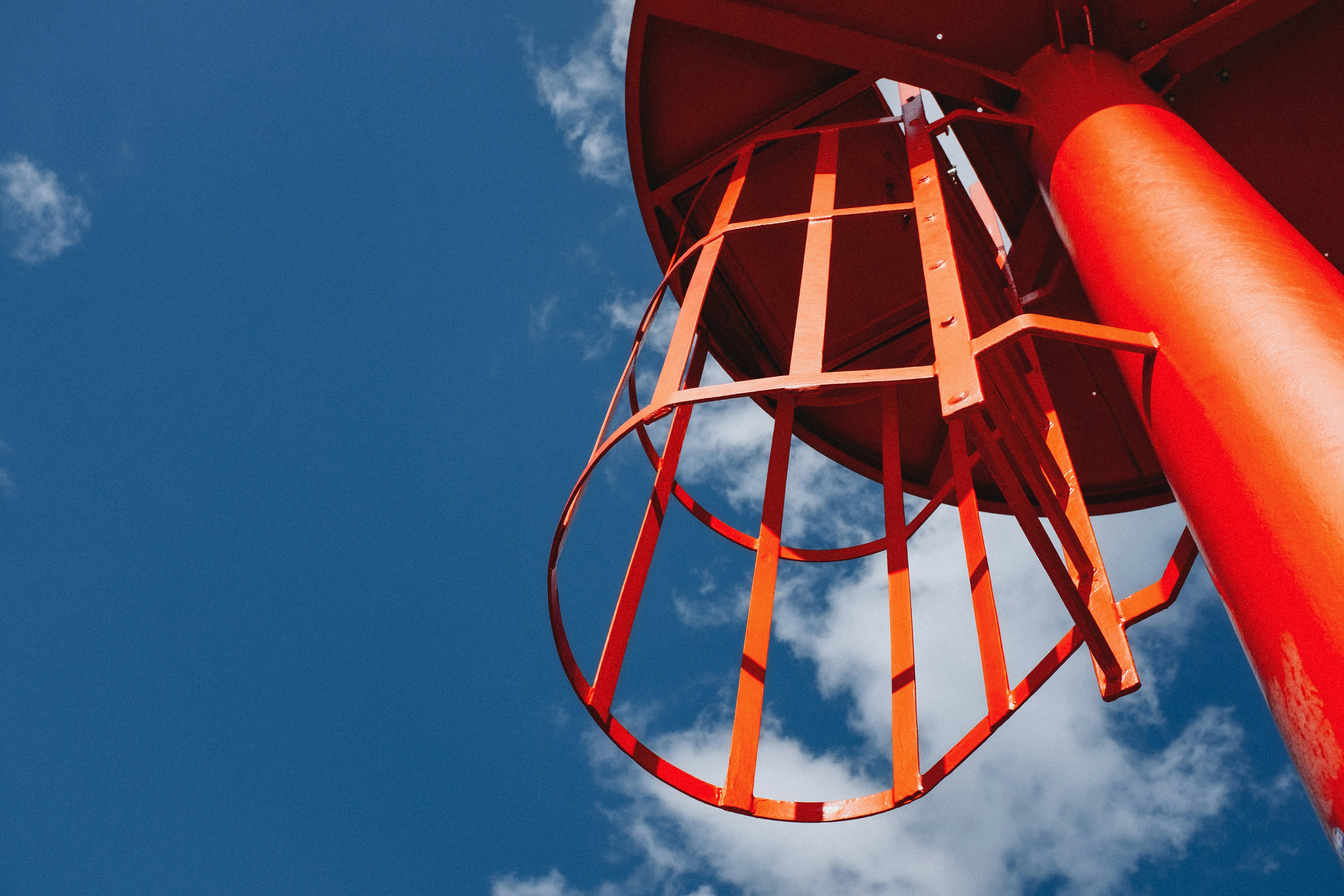 A striking red spiral staircase under a clear blue sky, emphasizing geometric shapes and vibrant color contrasts.