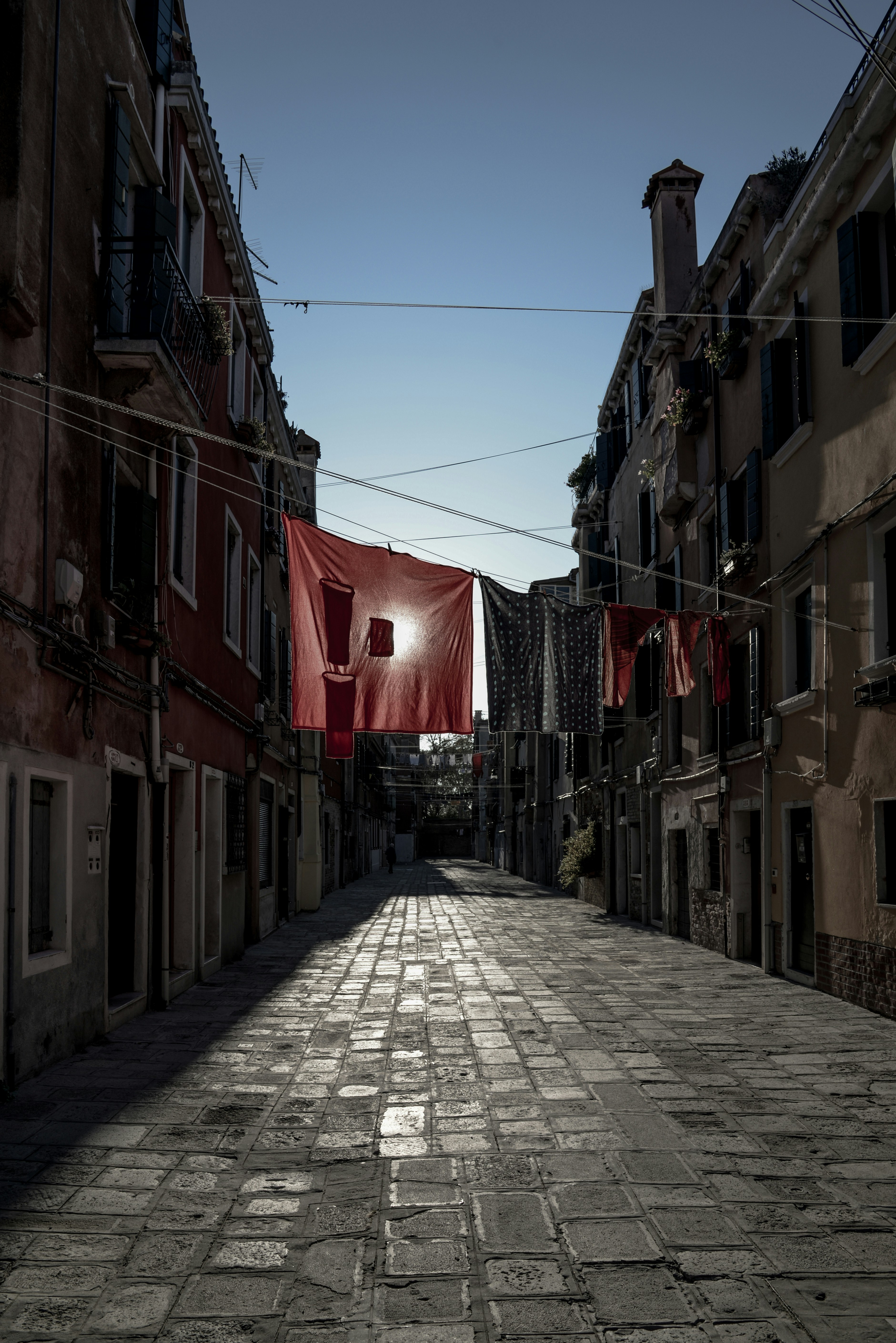 Sunlit Laundry Hallway: A Narrow Italian Street Draped in Red Cloths
