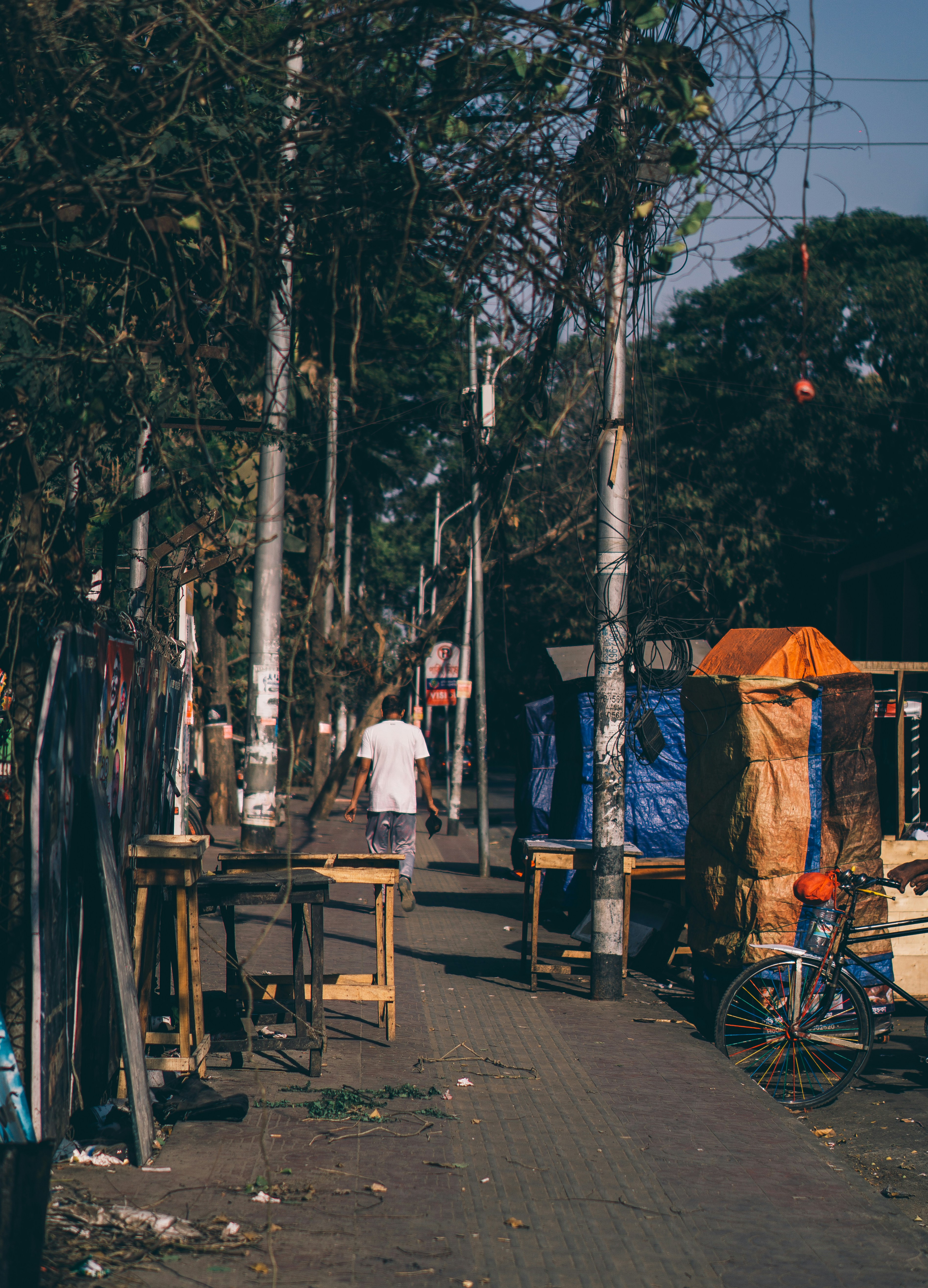 A quiet street market scene featuring wooden stalls and vibrant tarps, with a lone figure walking down the path. The atmosphere reflects a blend of commerce and community.