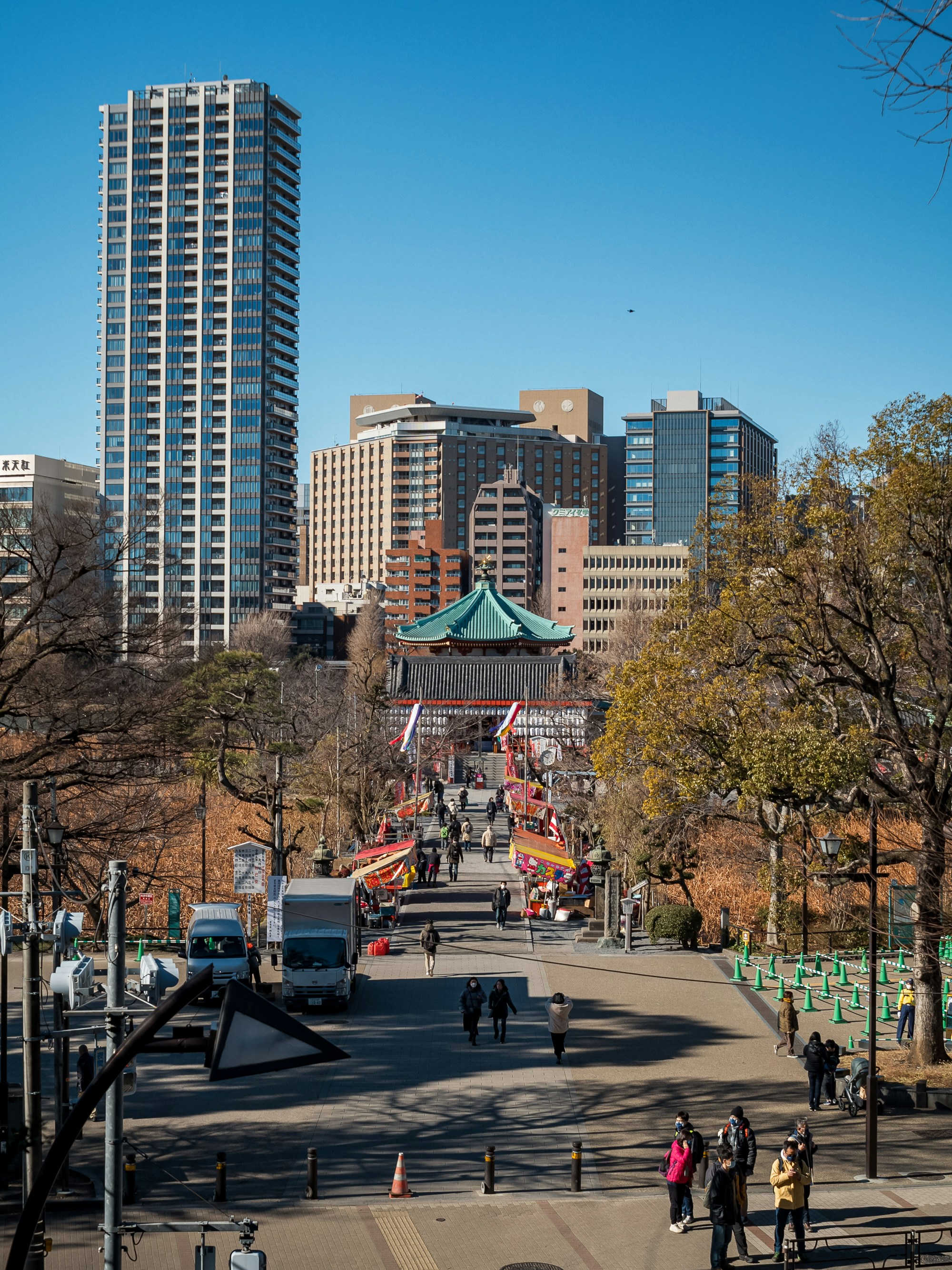 A daytime street view toward a traditional temple gate framed by modern high-rises, with pedestrians along a wide avenue. This photograph captures a juxtaposition of old and new in clear daylight.