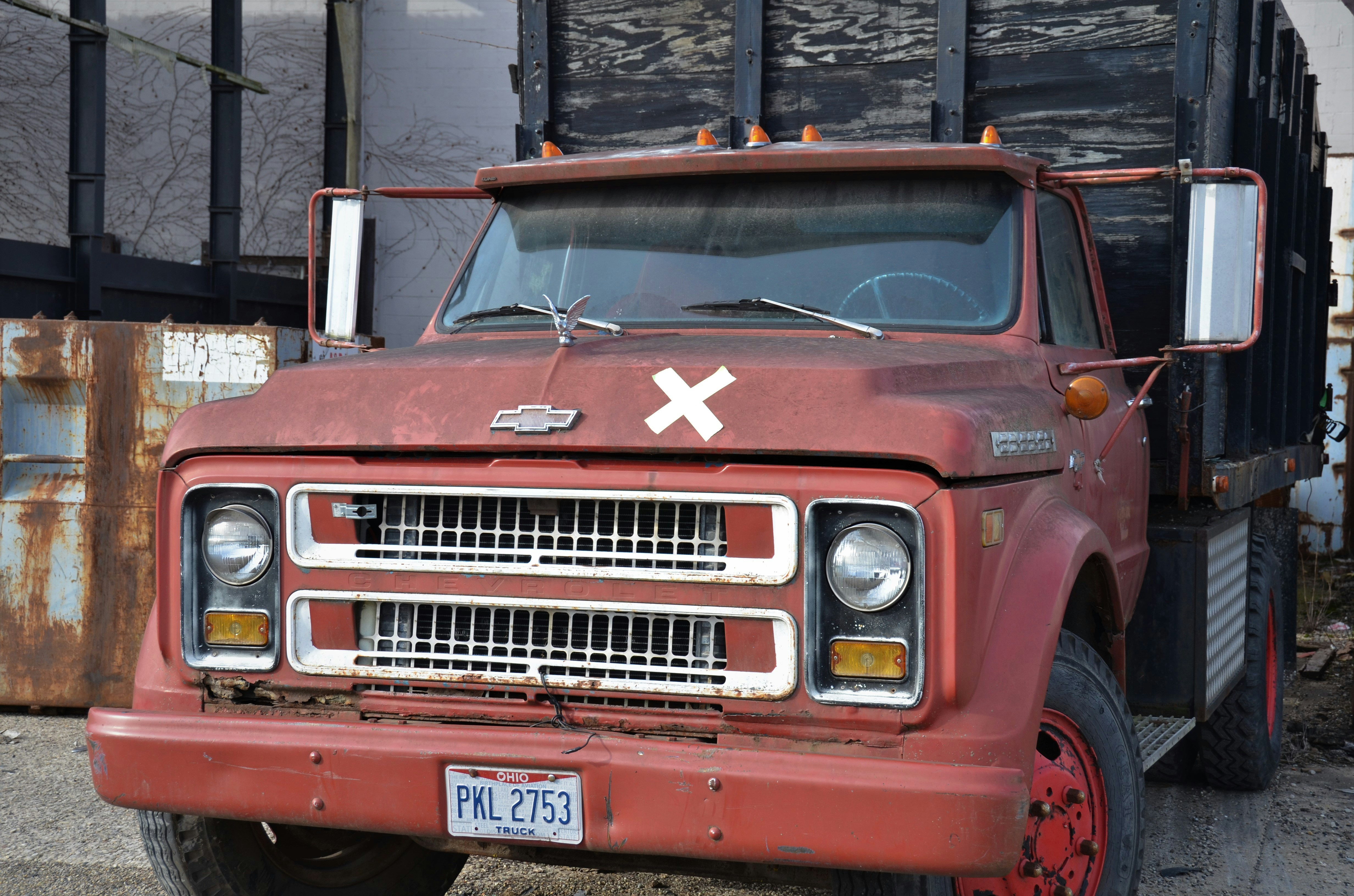 Crimson Workhorse in a Rust-Pocked Yard: Front View of a Weathered Dump Truck