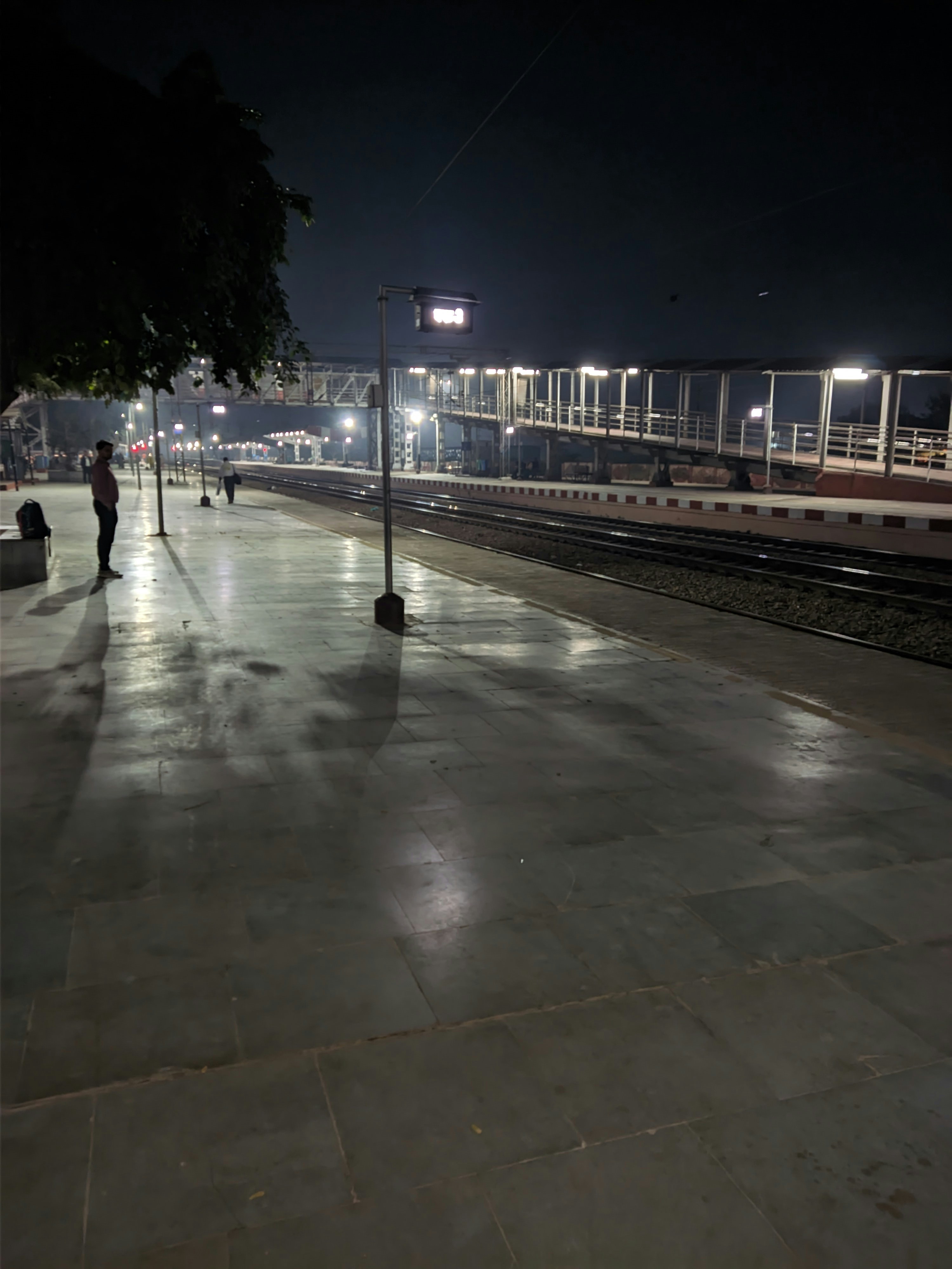 Dimly lit train platform at night with empty tracks and a solitary figure in the distance.