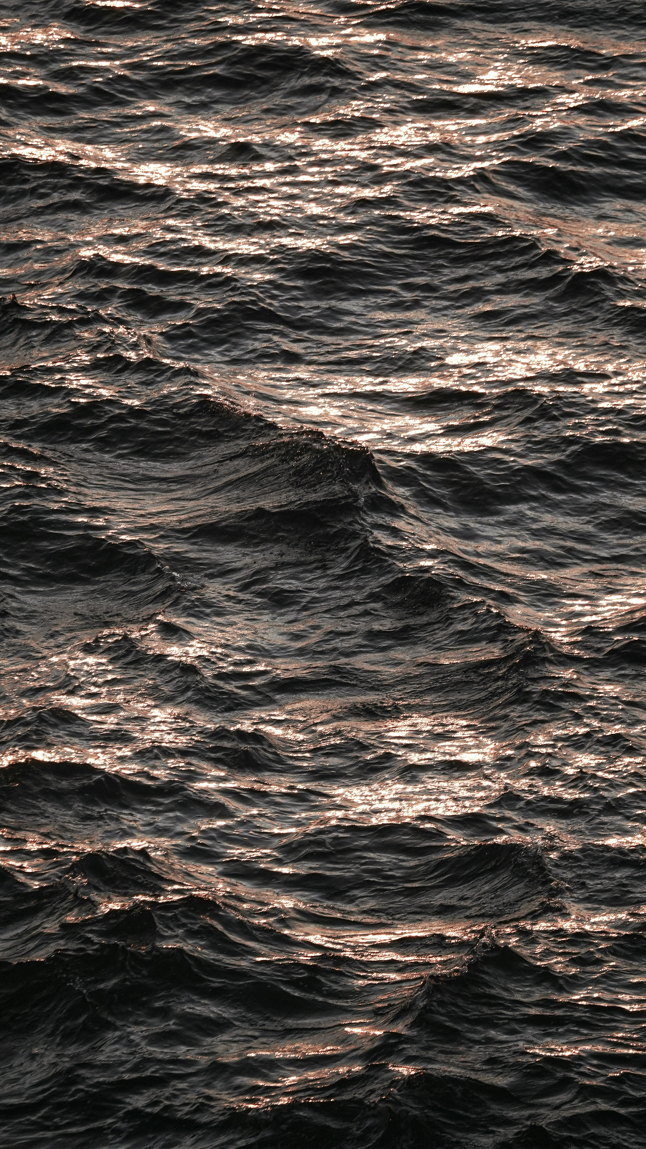 Rippling ocean waves reflect soft light, creating a mesmerizing interplay of shadows and glimmers. The image captures the serene essence of water in motion.