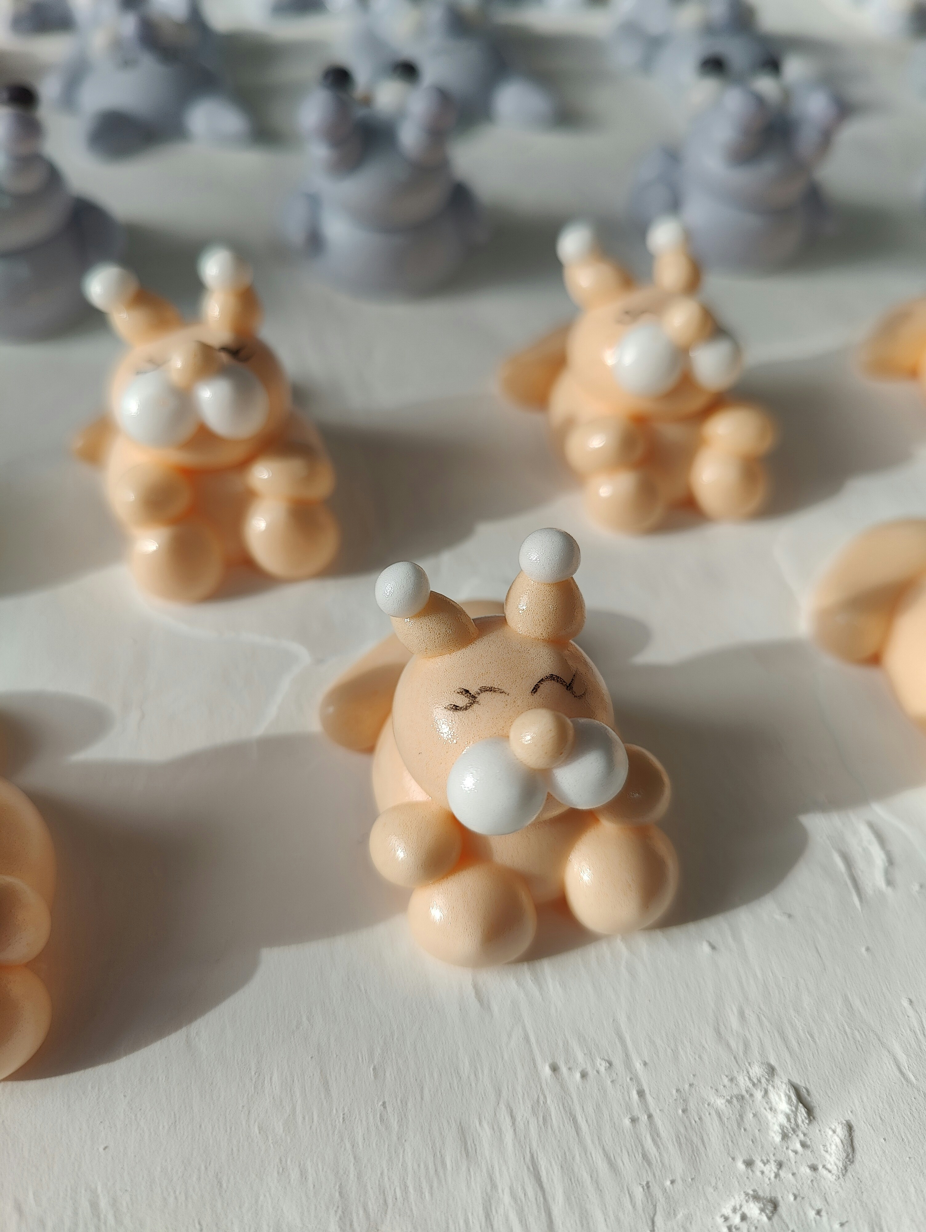 Row of small, pastel-colored clay bunny figurines on a white surface, with a foreground bunny in clear focus and others fading into the background; a playful tabletop scene.