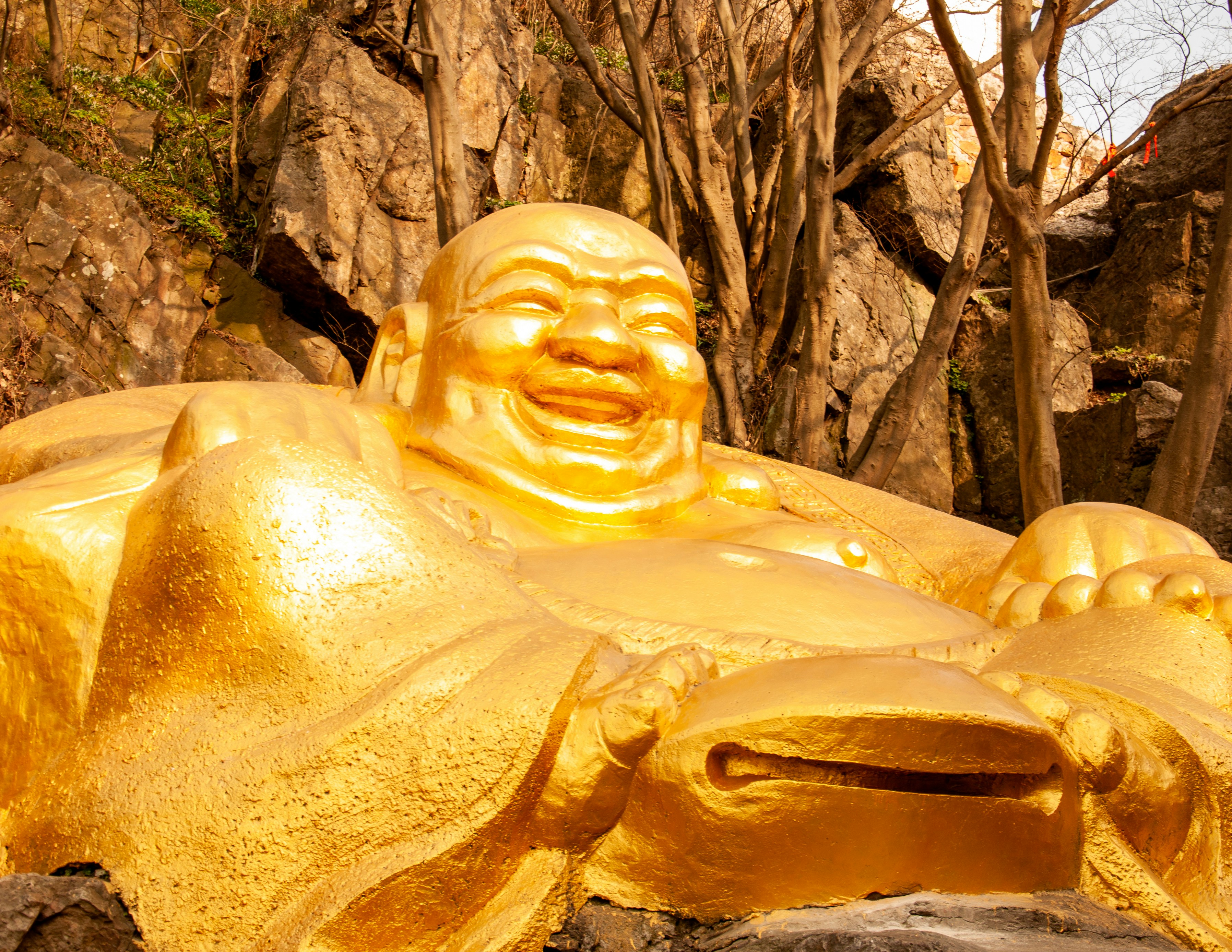 Golden statue of a smiling figure reclining against rugged rock formations.