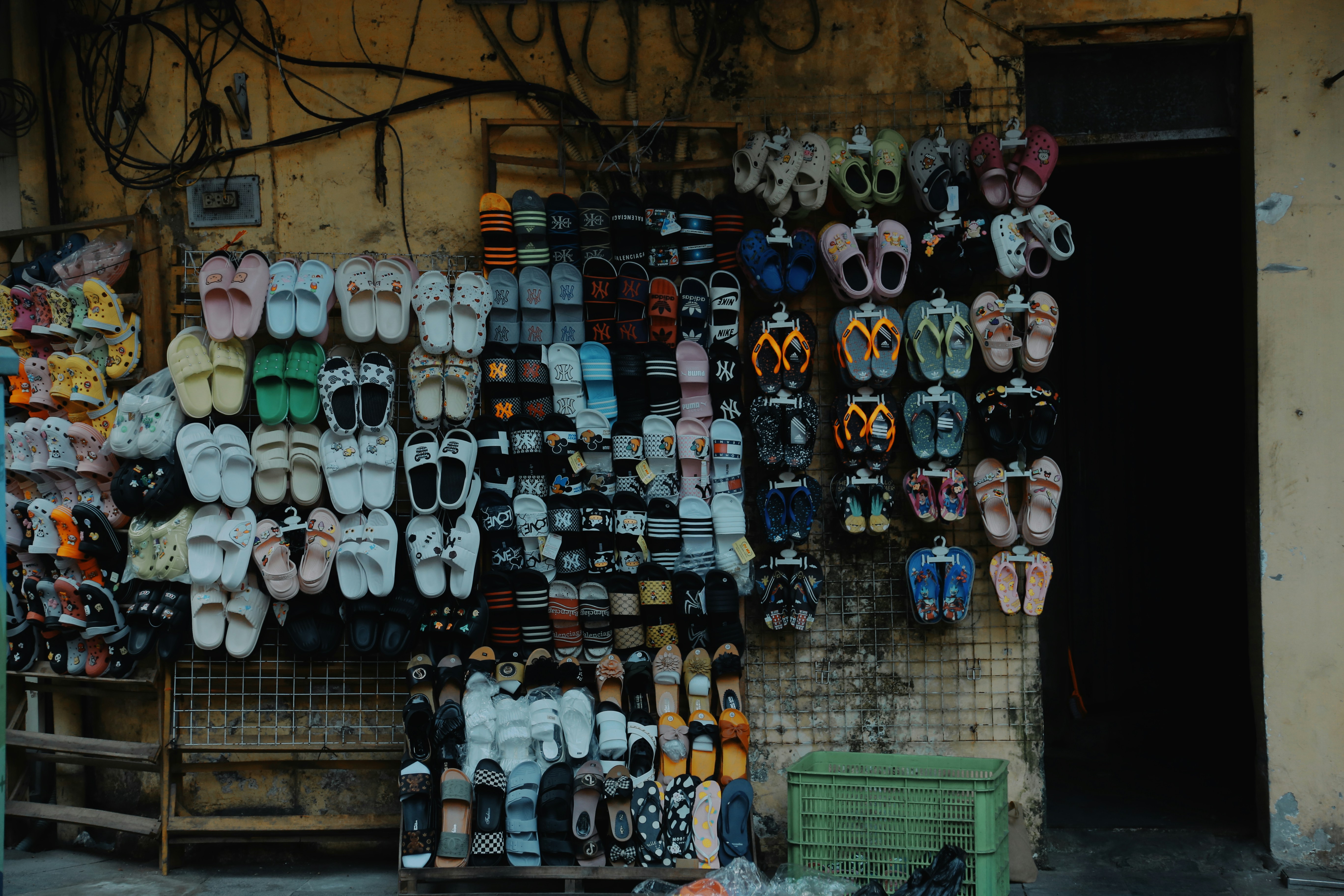 A colorful array of flip-flops and sandals displayed on a market wall, showcasing a variety of styles and designs. The scene captures the essence of local commerce.
