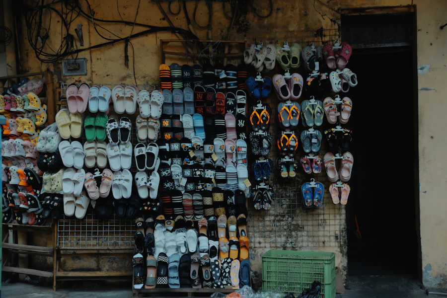 Rows of colorful sandals hang on a weathered wall beside a dark doorway and a green crate. The display fills most of the frame in a market-like setting.