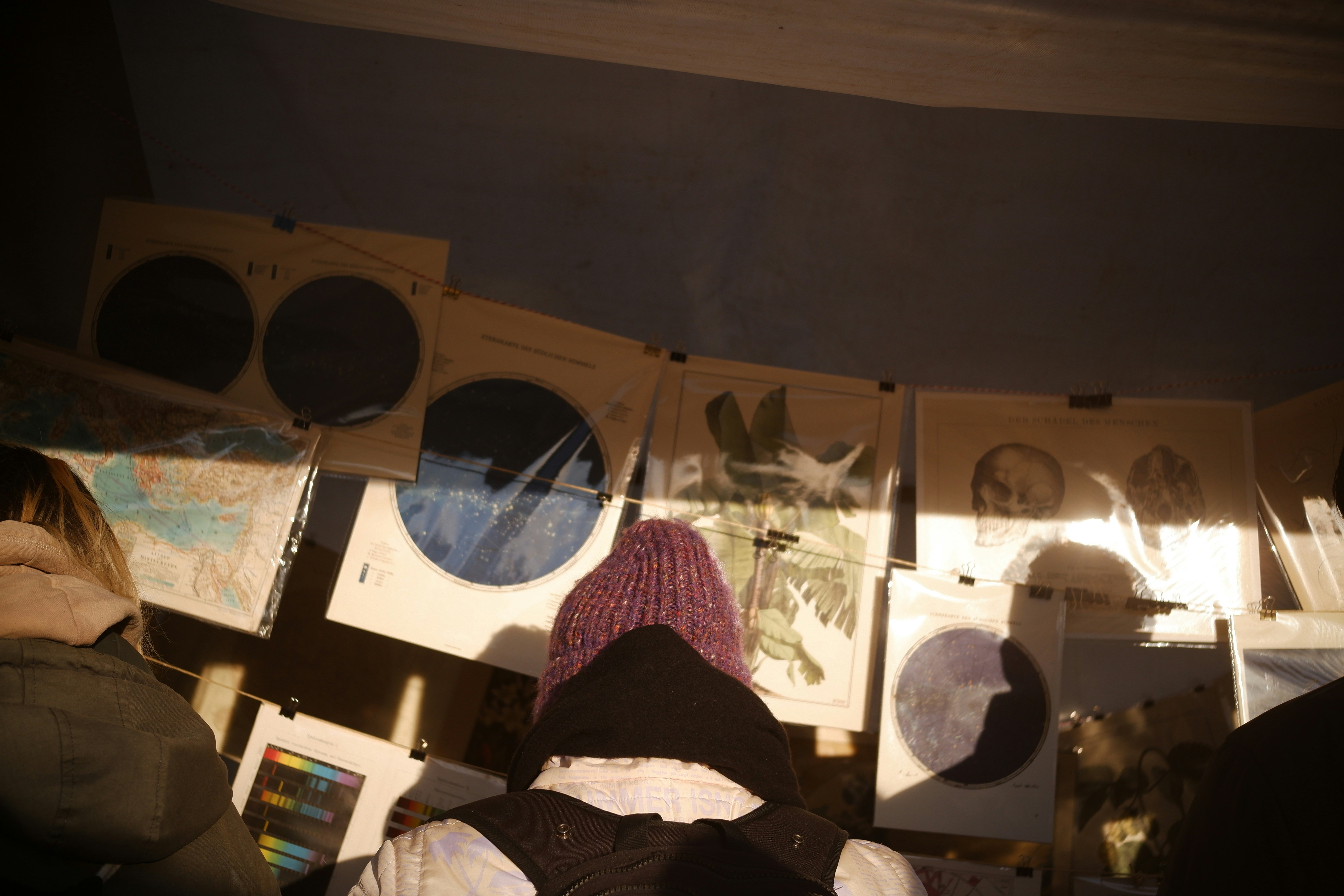 Purple-hatted Viewer Navigates a Wall of Circular Portraits in Warm Gallery Light