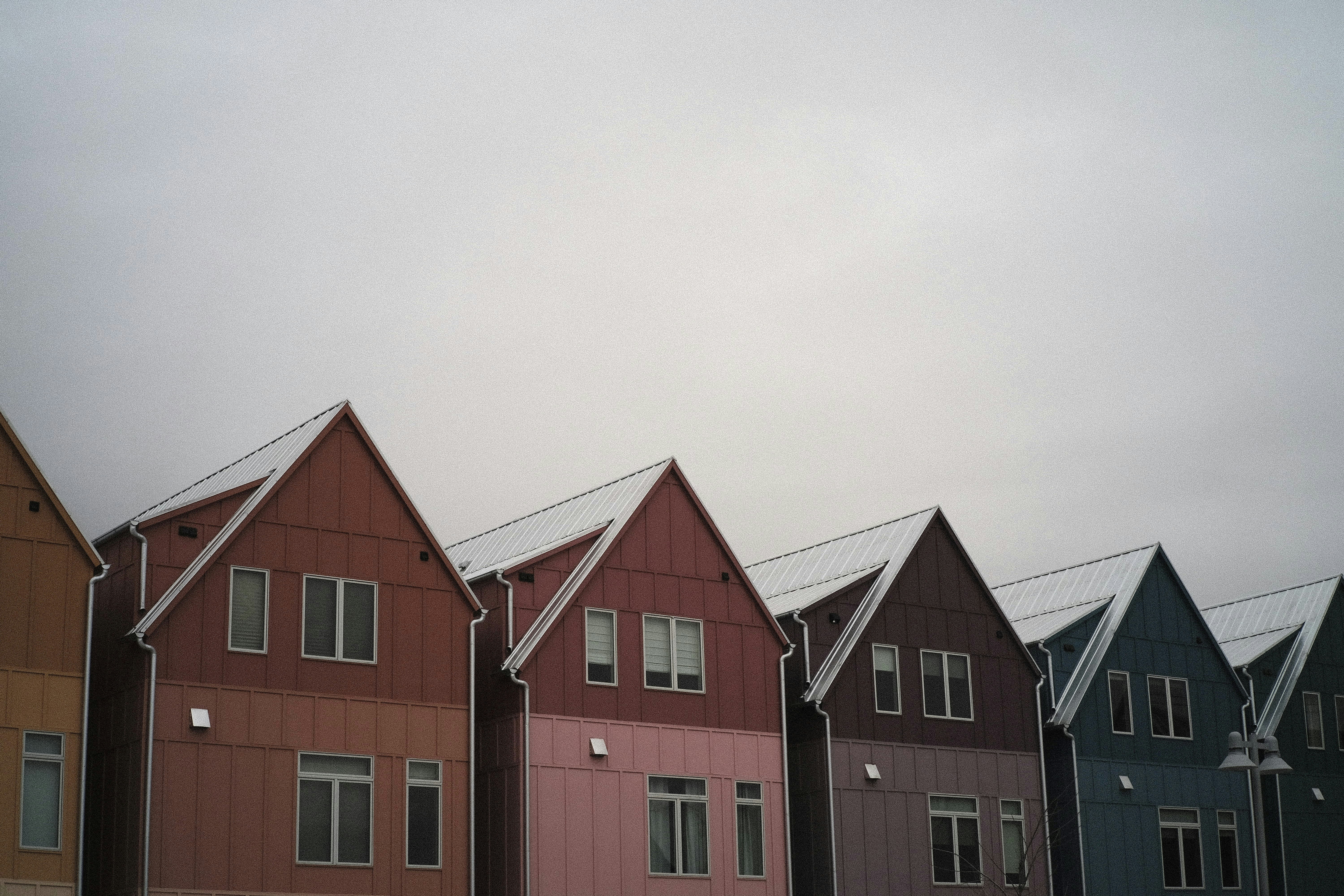 Colorful modern houses with sloped roofs lined up against a gray sky, showcasing a blend of architectural styles and hues.