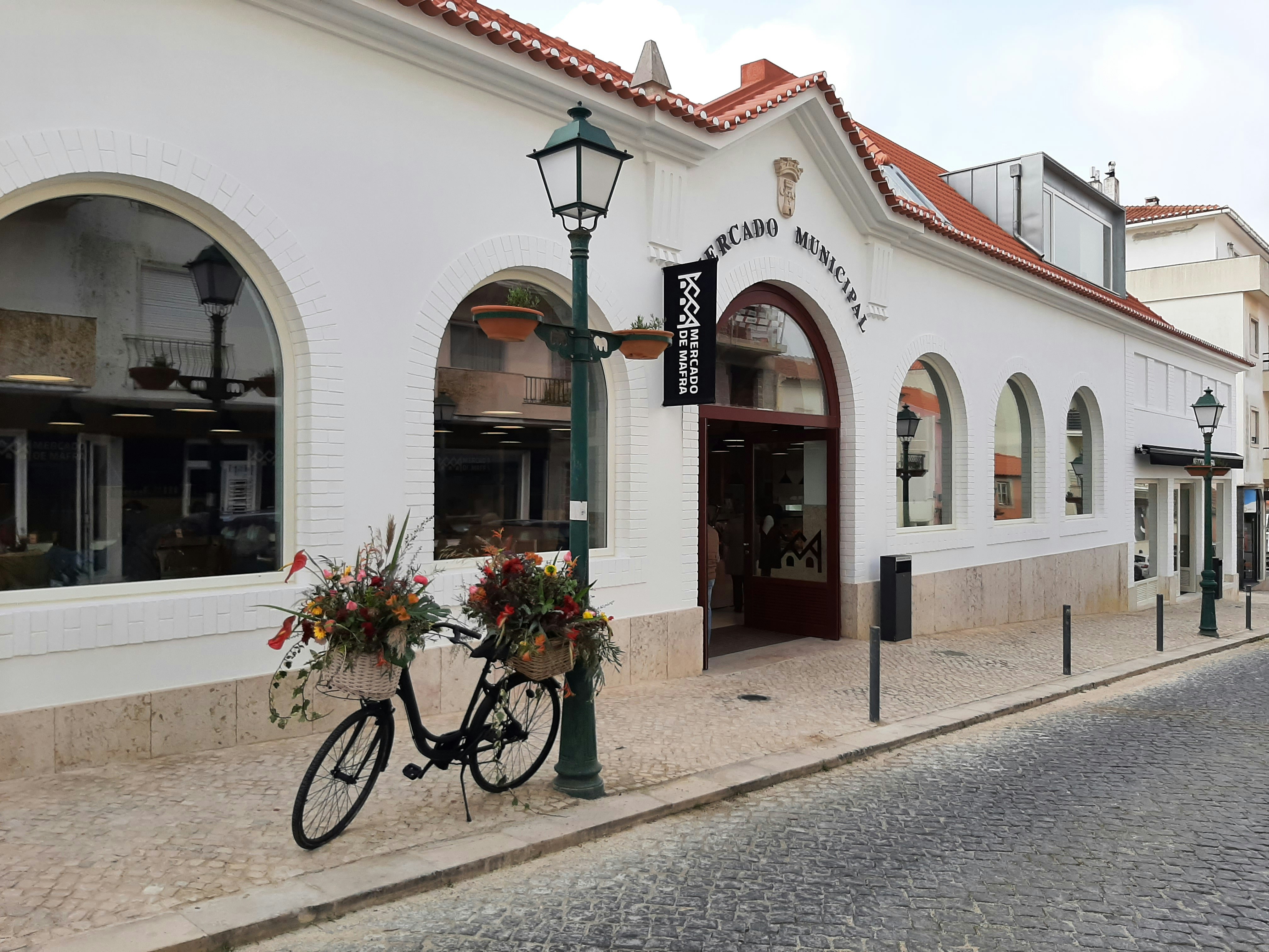 White building with arched windows and a vintage bicycle adorned with flowers on a cobblestone street.
