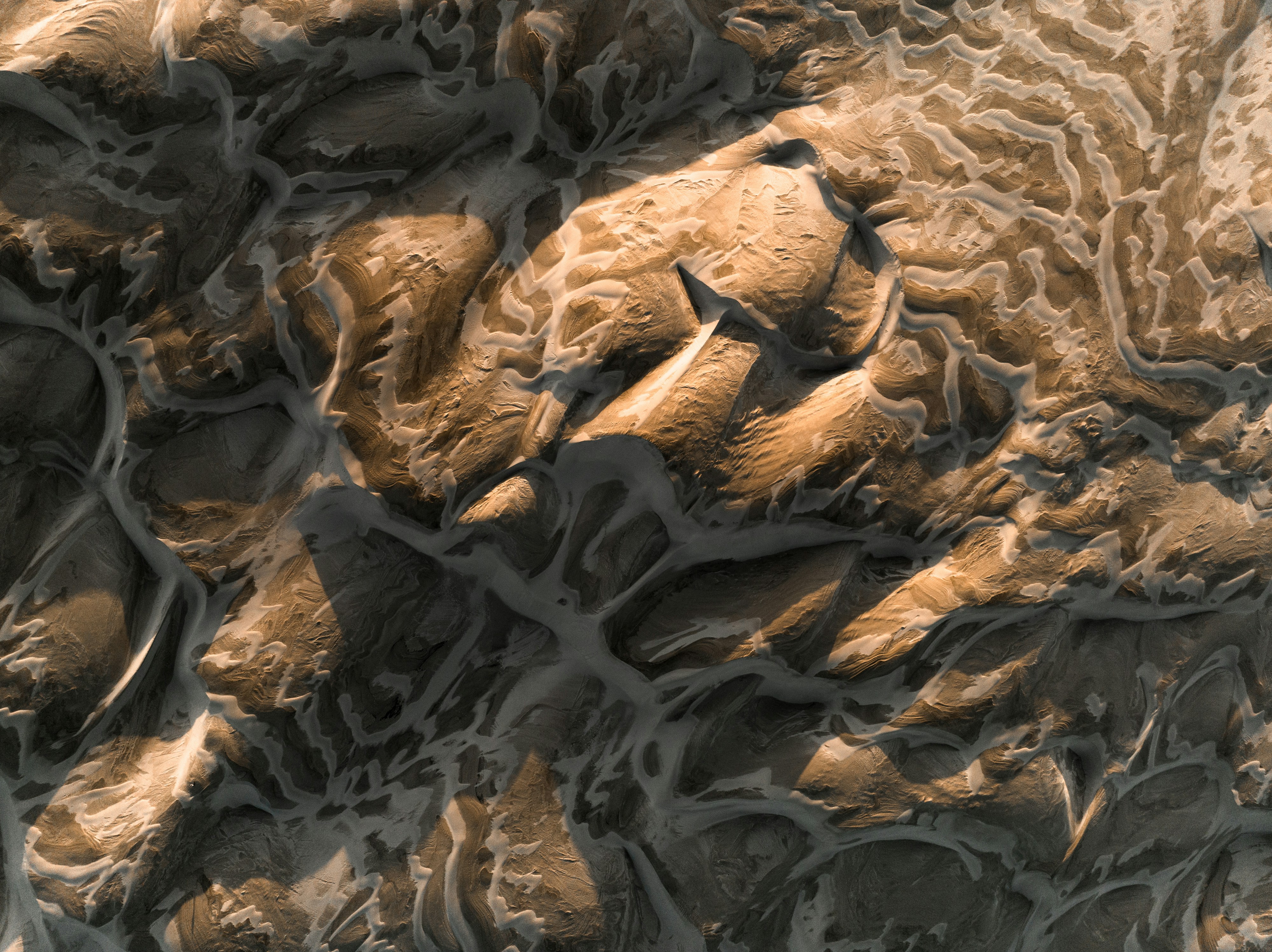 Sunlit sand dunes form intricate patterns resembling abstract art in a desert landscape.