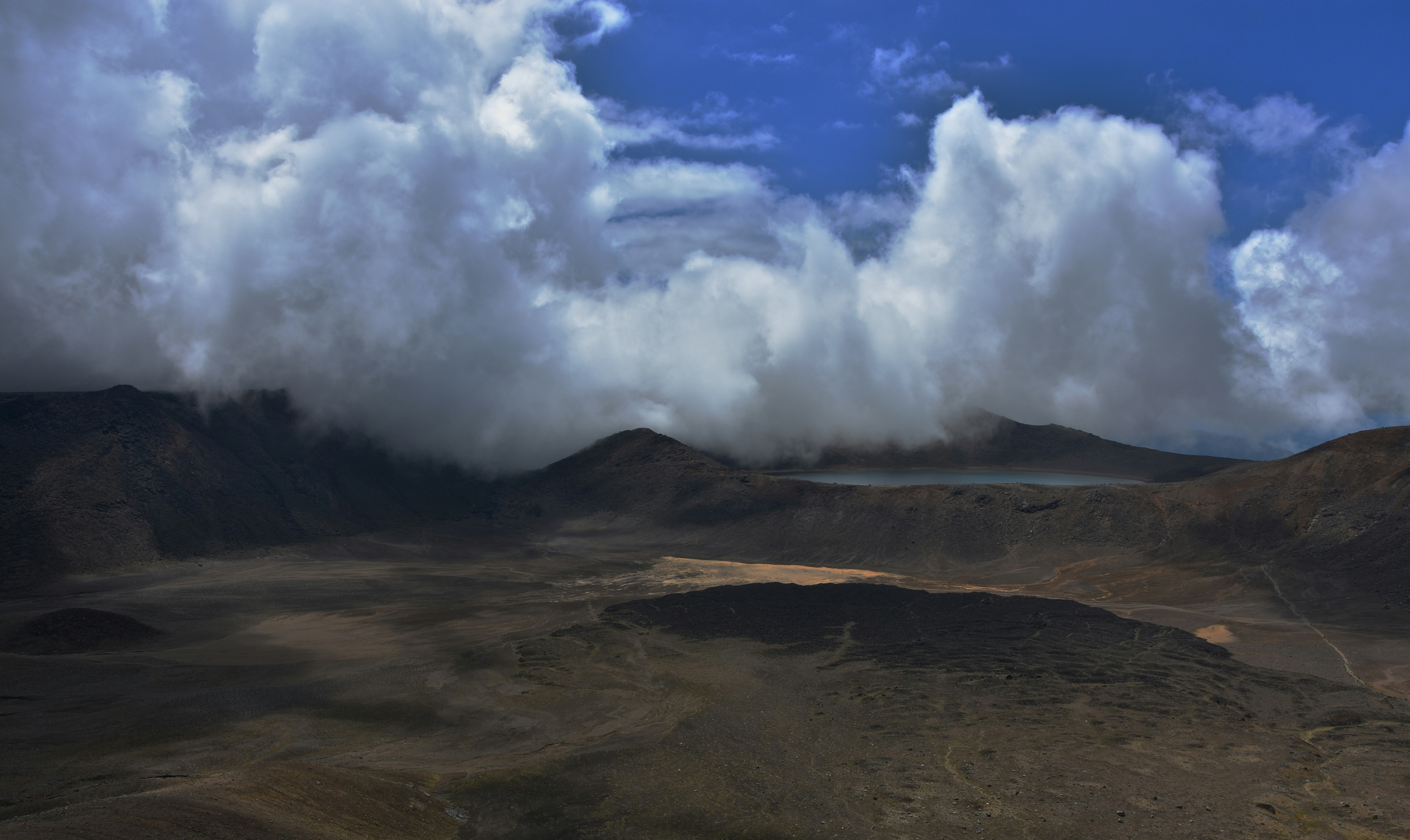 Expansive clouds hover above a rugged volcanic landscape under a deep blue sky.