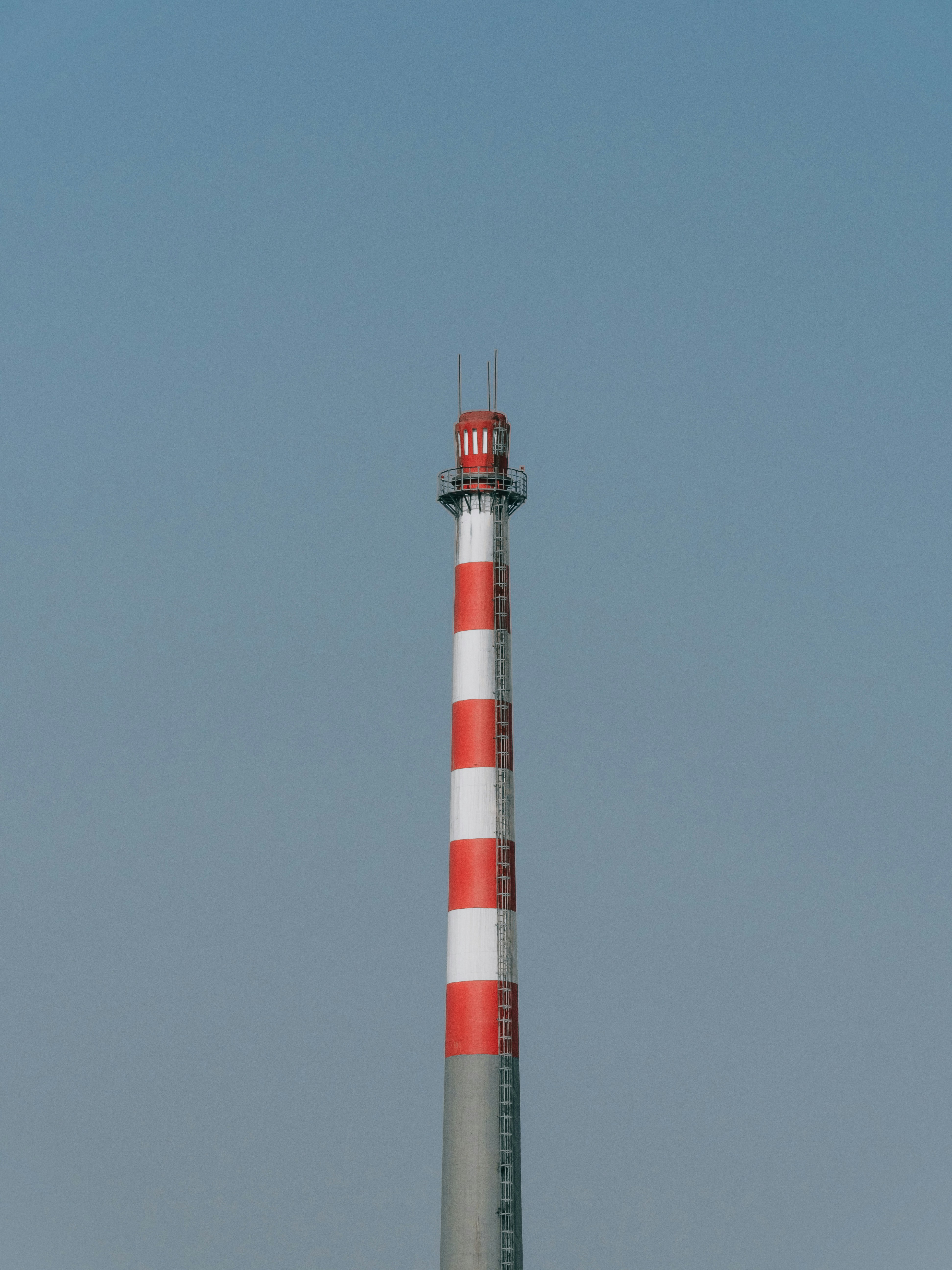 A tall industrial smokestack with alternating red and white stripes rises against a clear blue sky.
