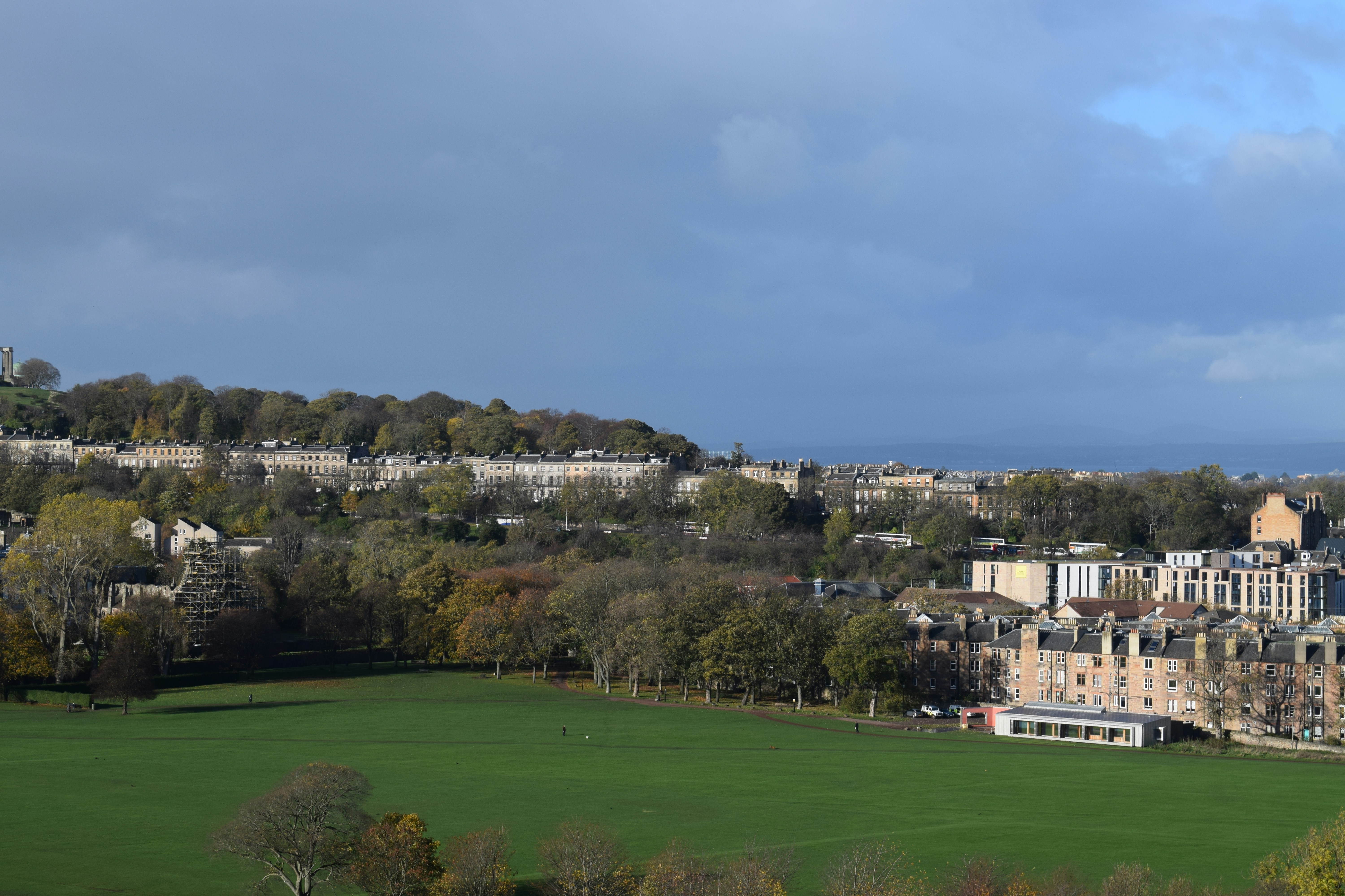 Cityscape with sprawling green fields under a cloudy sky.