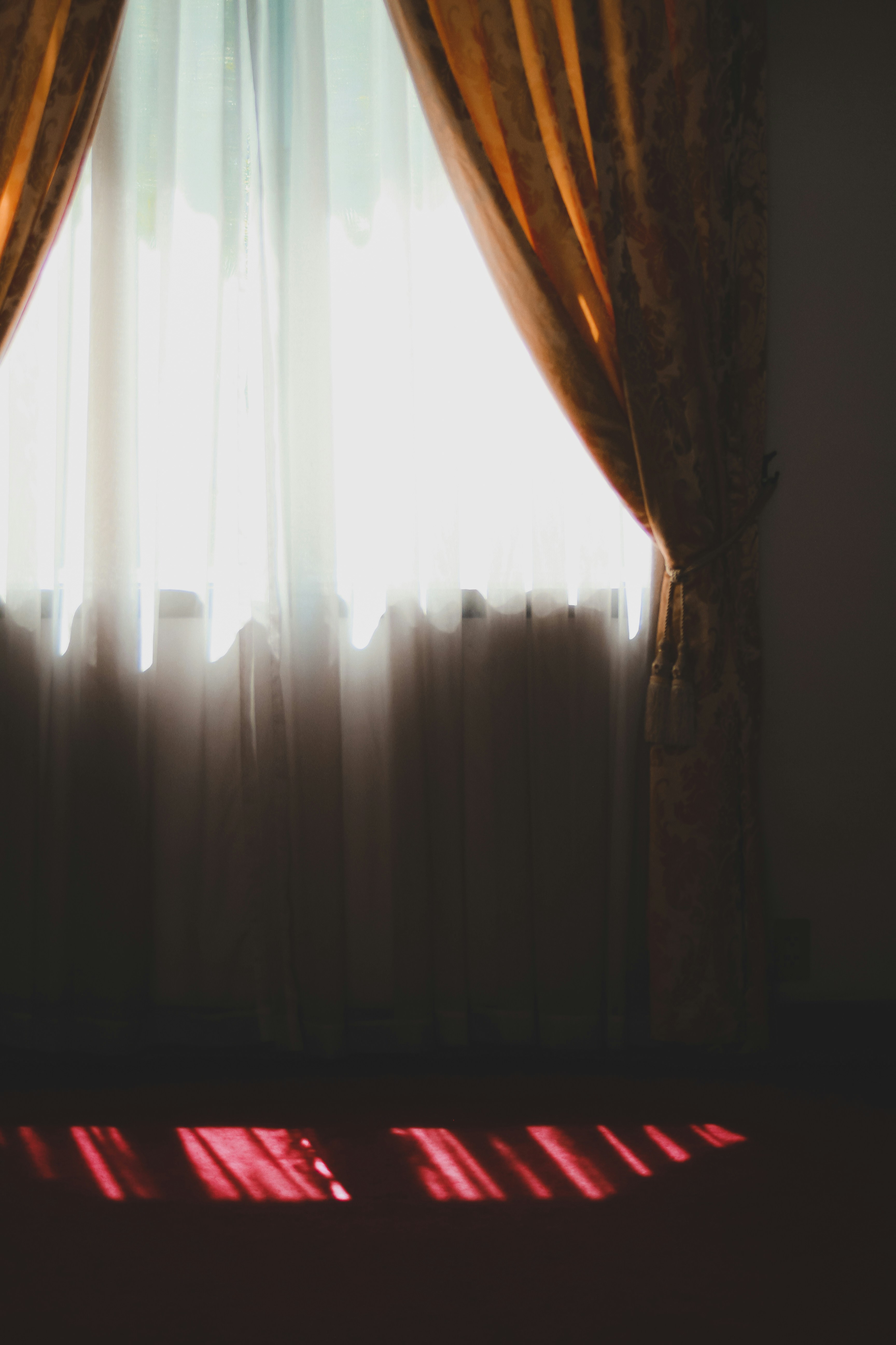 A window with a curtain and a red light coming through it photo – Free ...