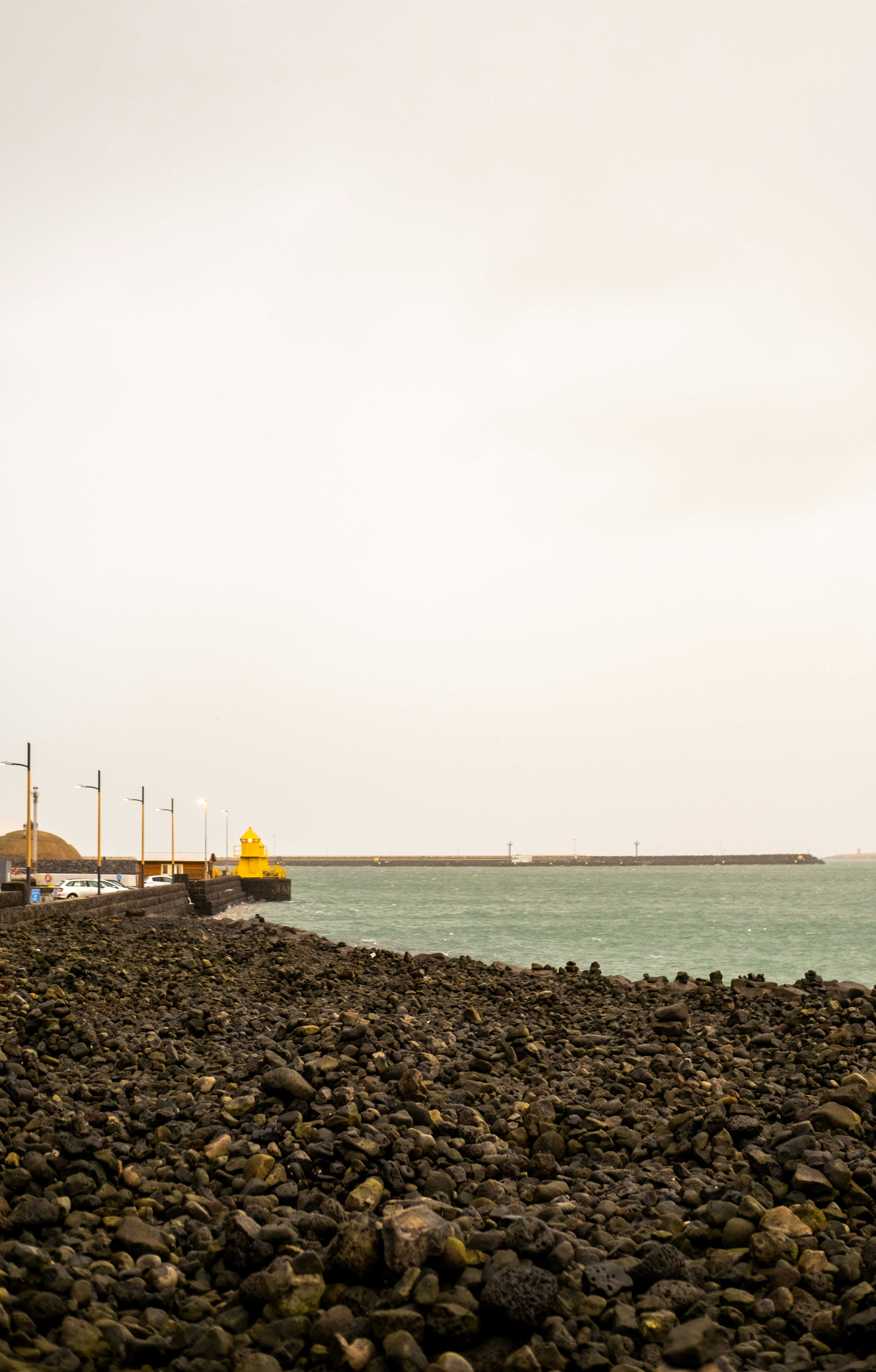 The Golden Beacon on a Pebble Pier Under a Soft Harbor Sky