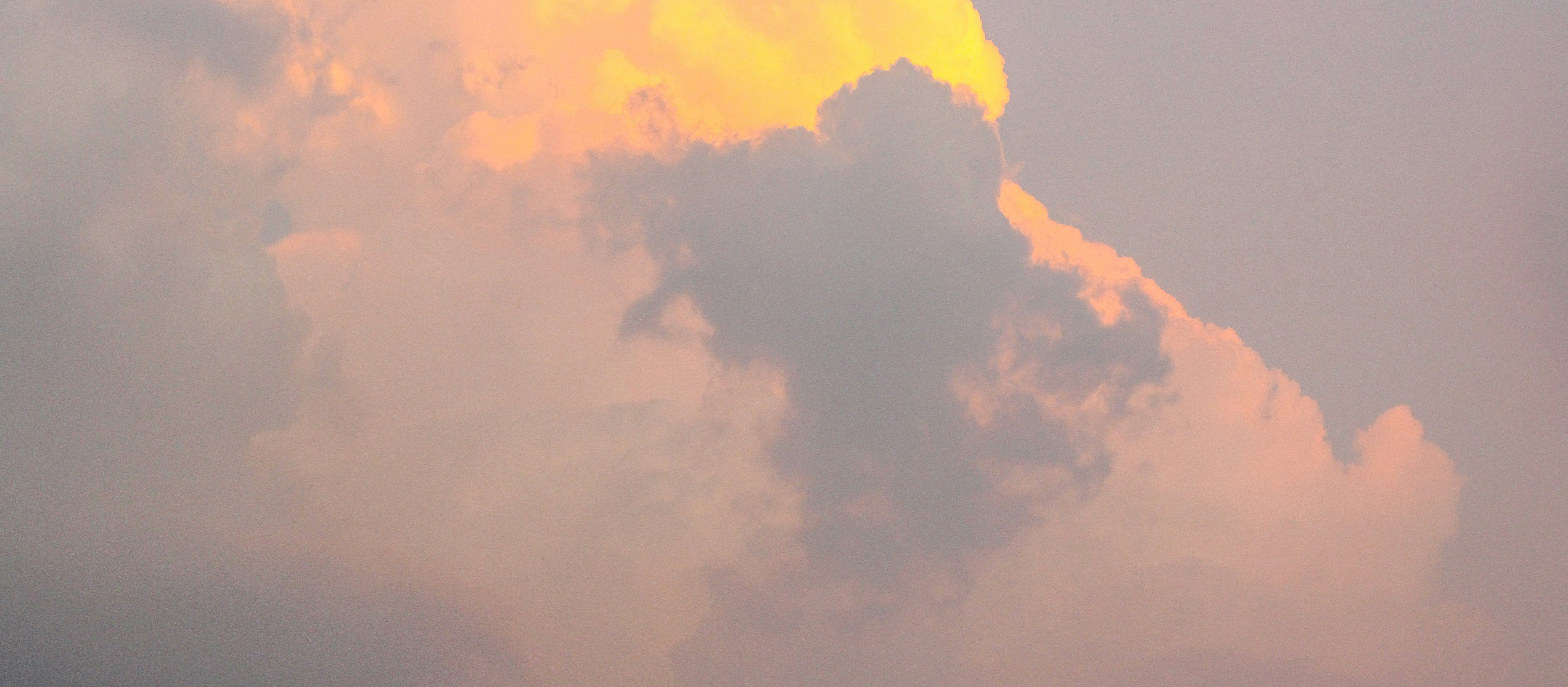 Golden-hued clouds illuminated by the setting sun against a soft pastel background.