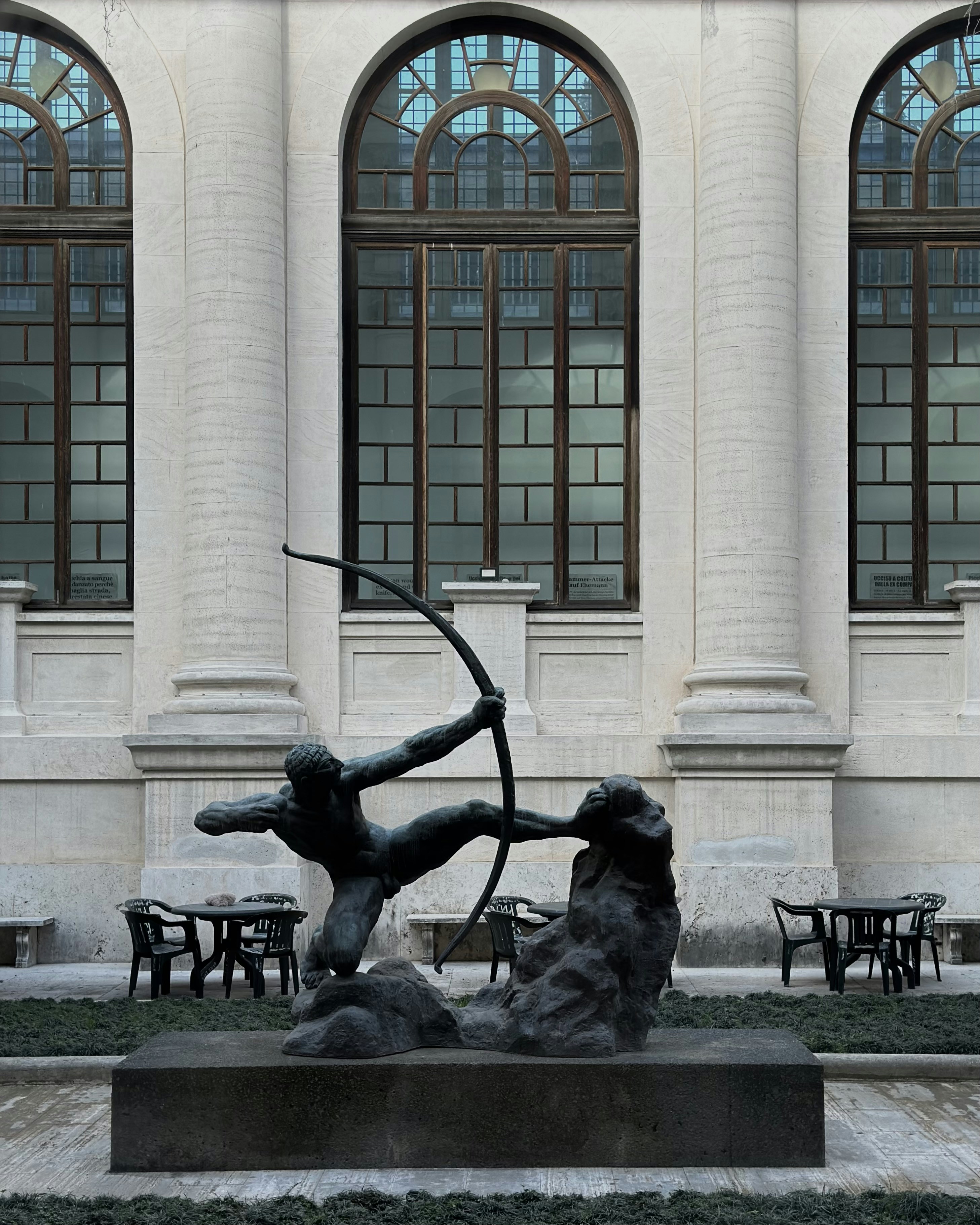 A statue of a man holding a bow and arrow in front of a building photo ...