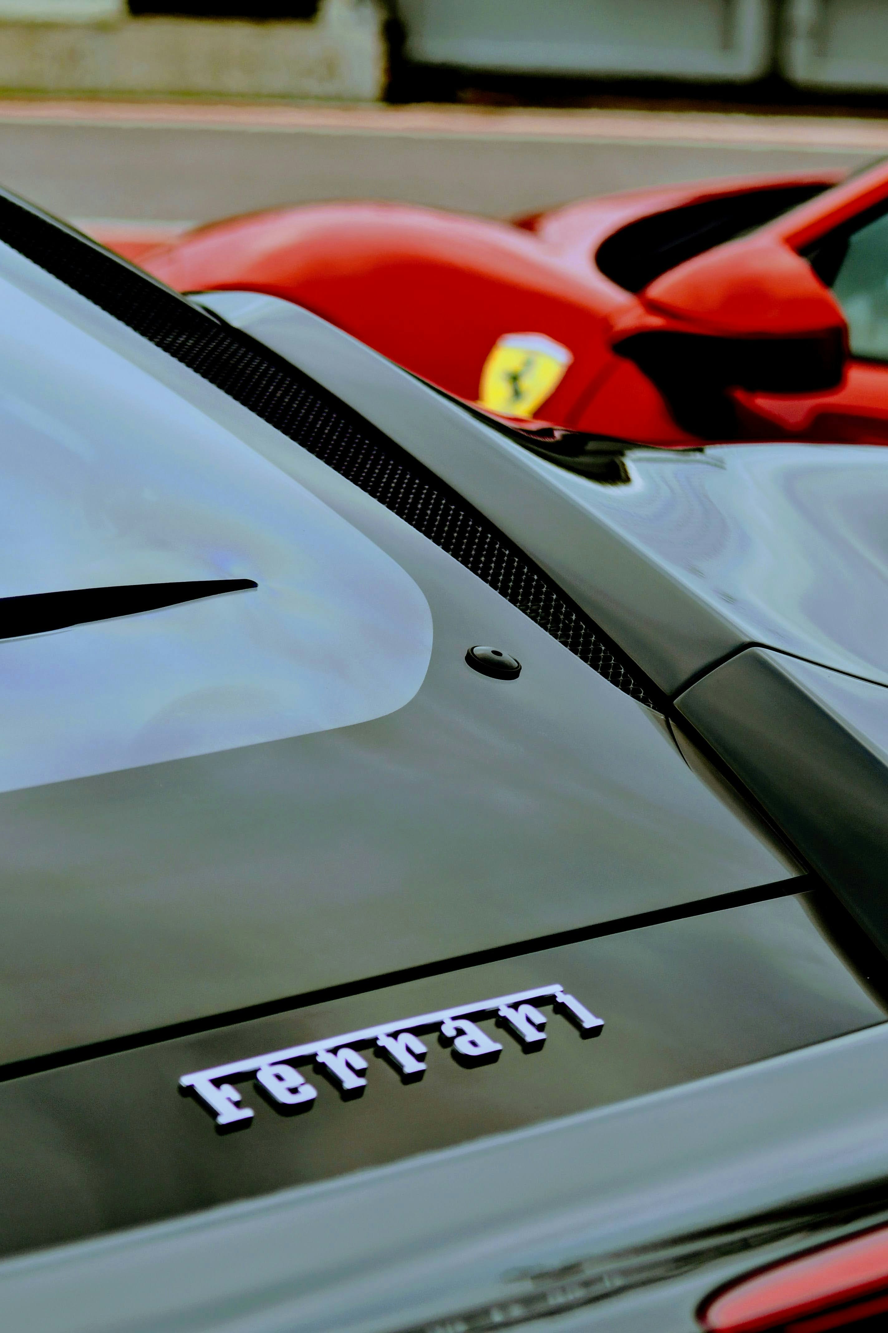 Close-up of a Ferrari badge on a sleek black car, with another Ferrari in the background. The image highlights the brand's iconic design and automotive prowess.