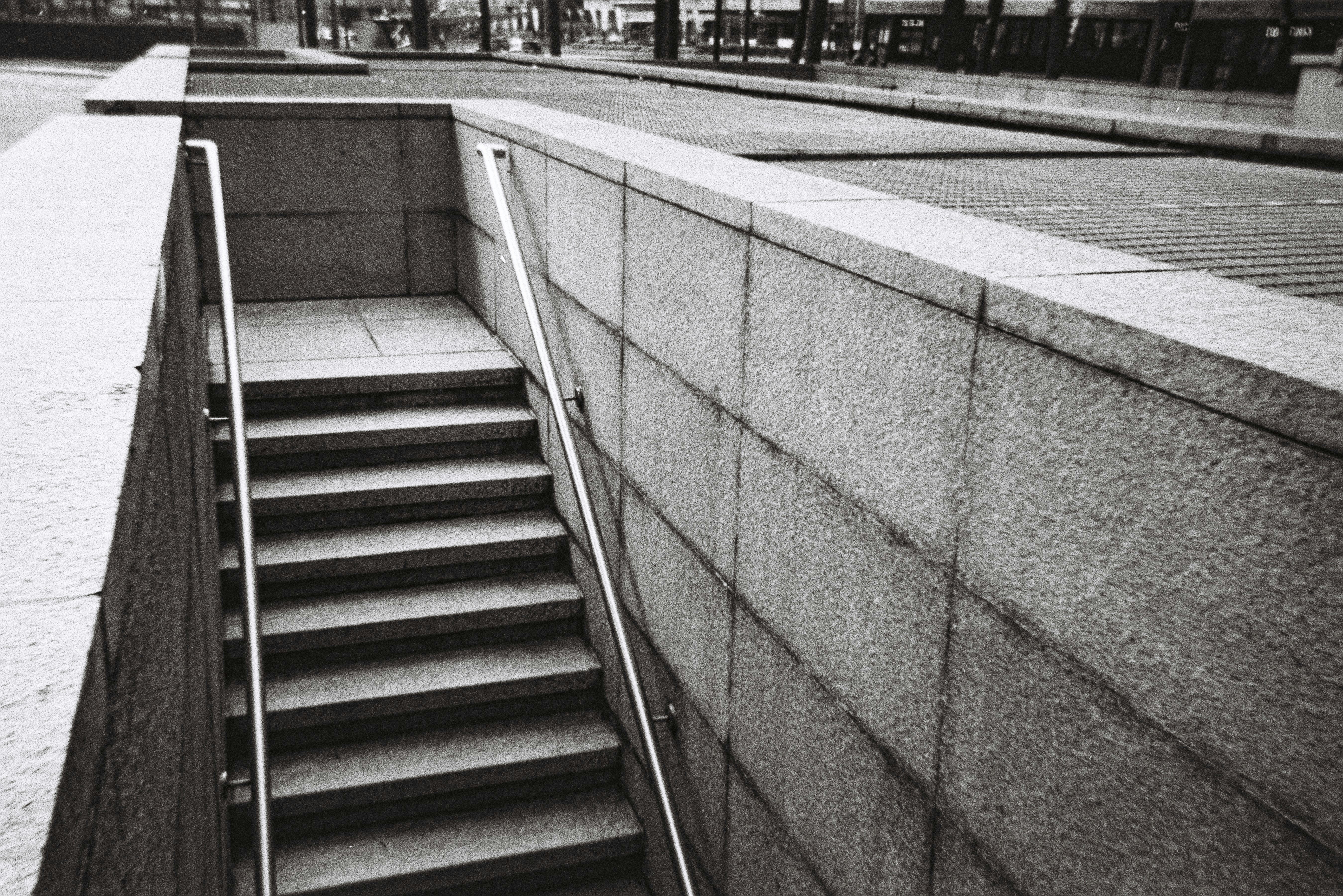 Monochrome staircase leading down between concrete walls in a cityscape.