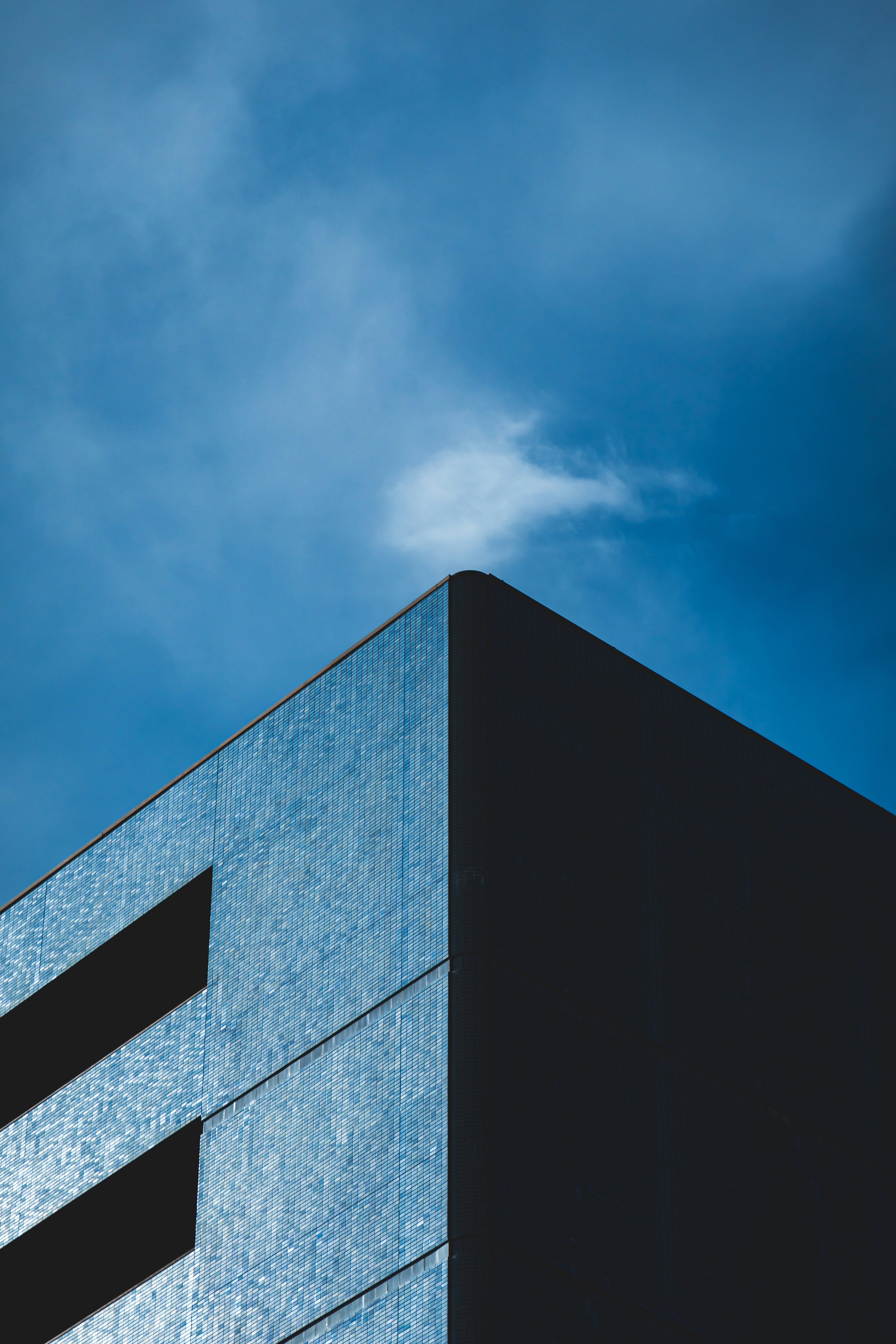 Modern architectural corner with geometric patterns reflecting sunlight under a blue sky.