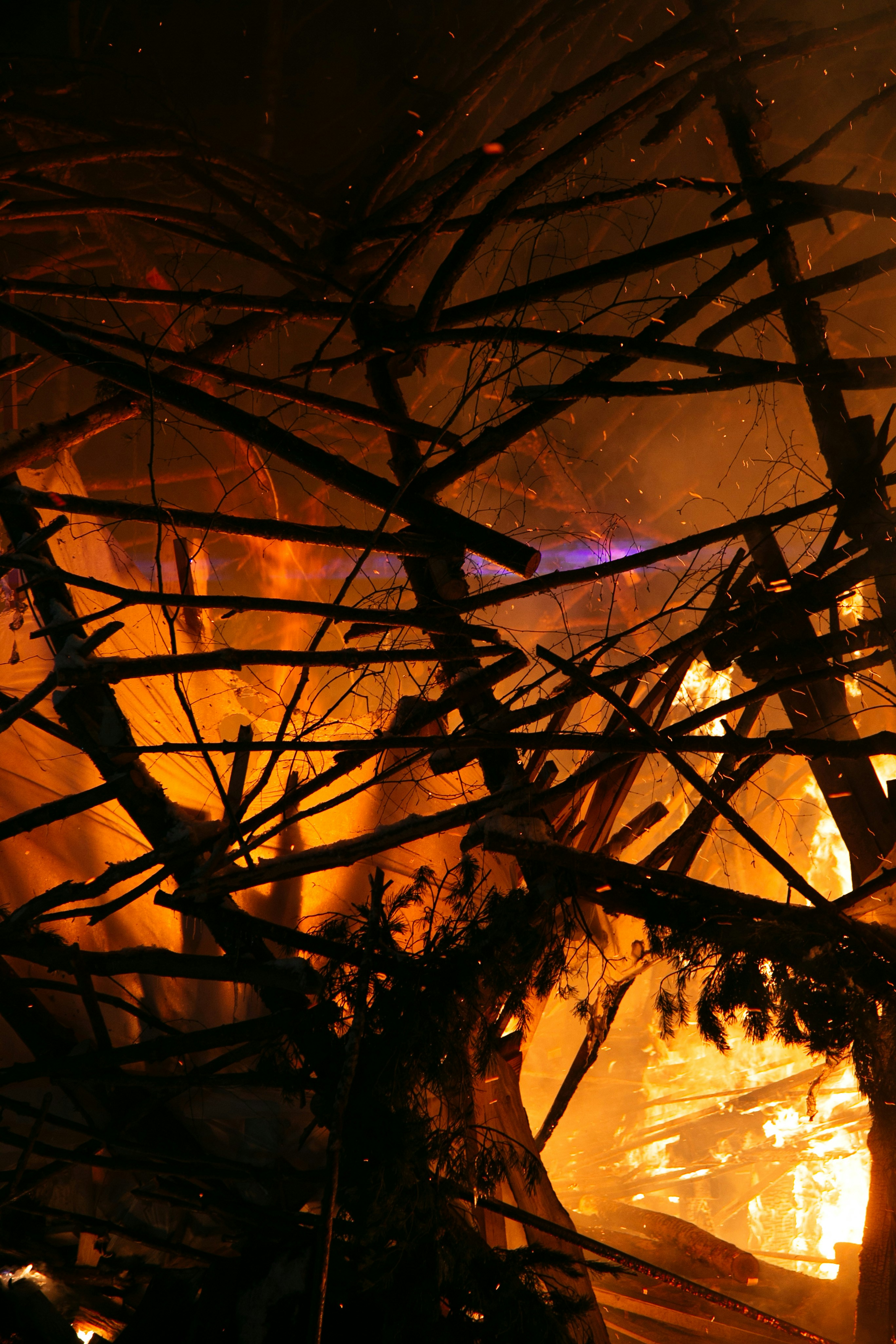 Flames erupting through a tangle of charred branches, illuminating the darkness with a fiery glow.