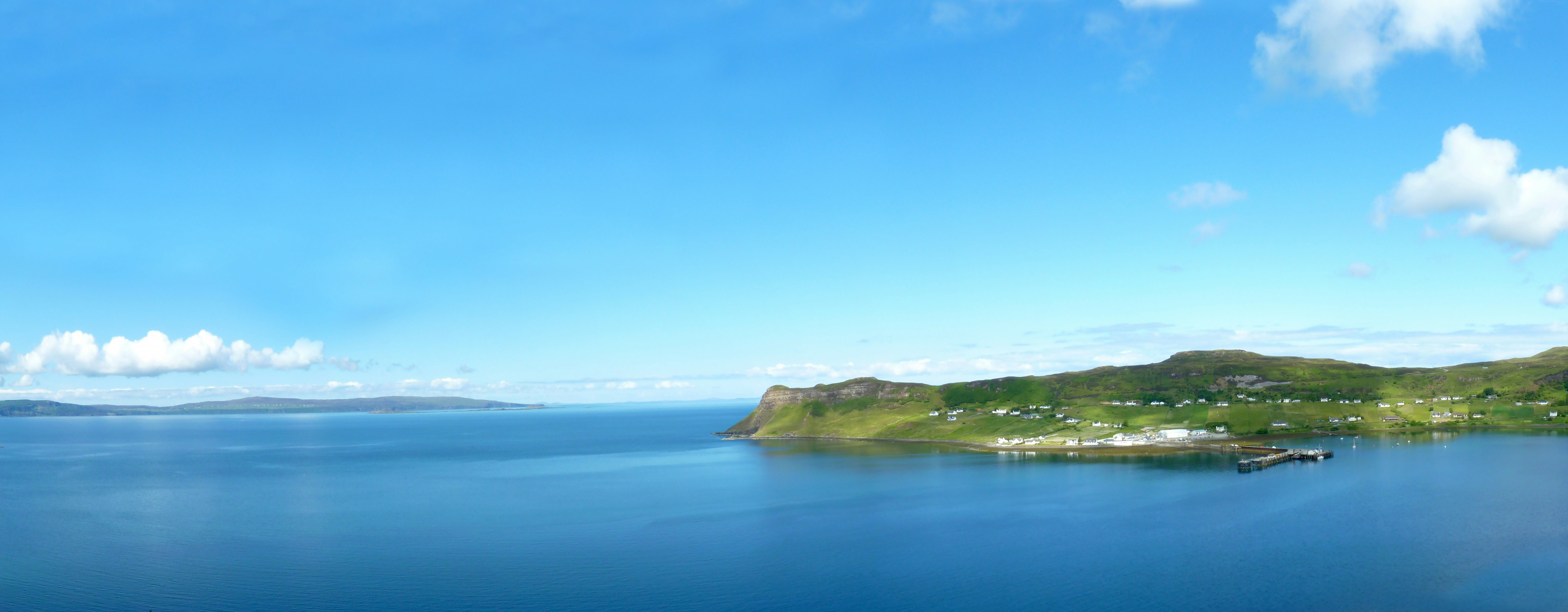 Vast ocean bay with a grassy peninsula under a clear blue sky.