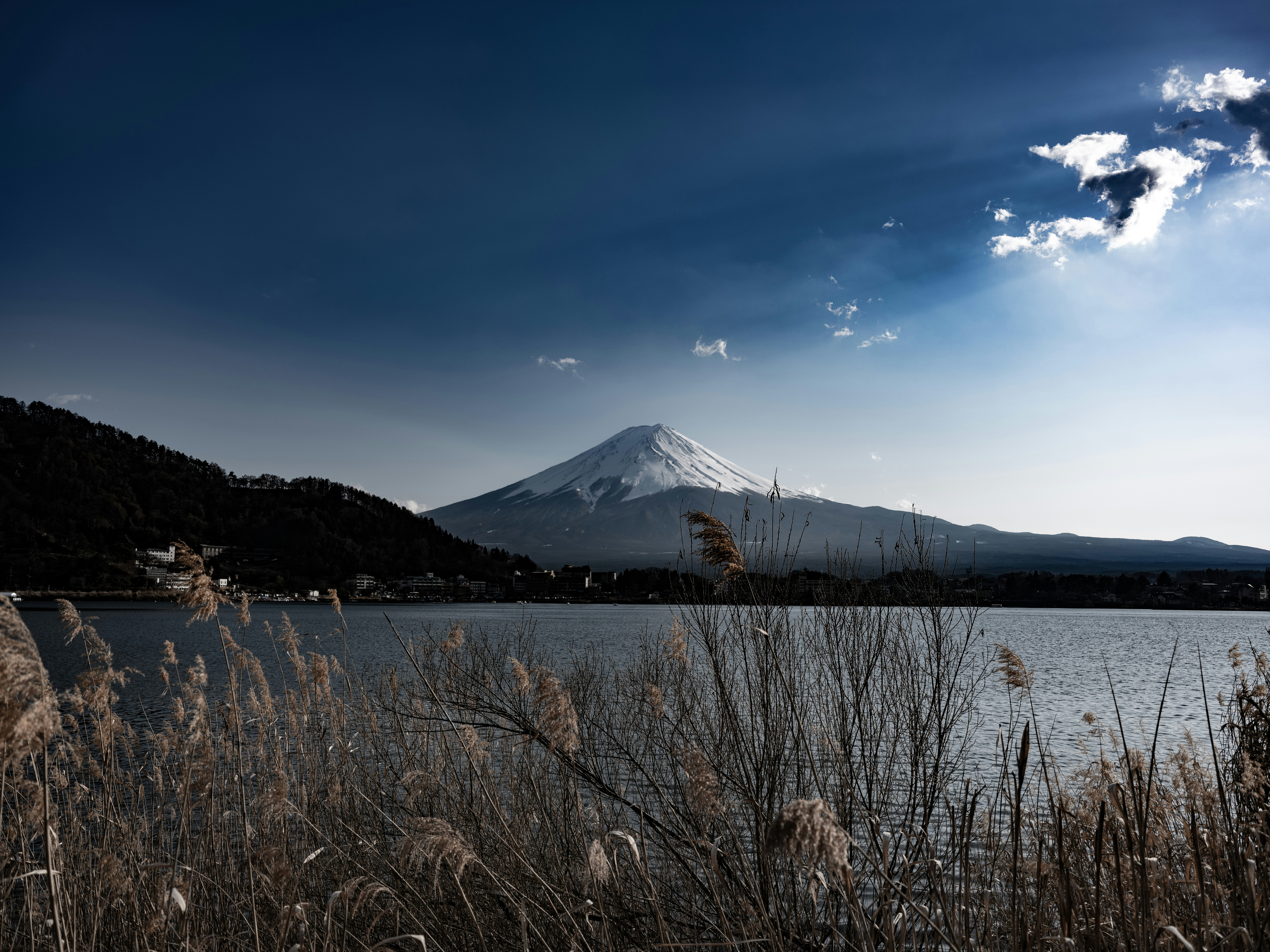 Snow-covered mountain reflected in a tranquil lake under a deep blue sky.