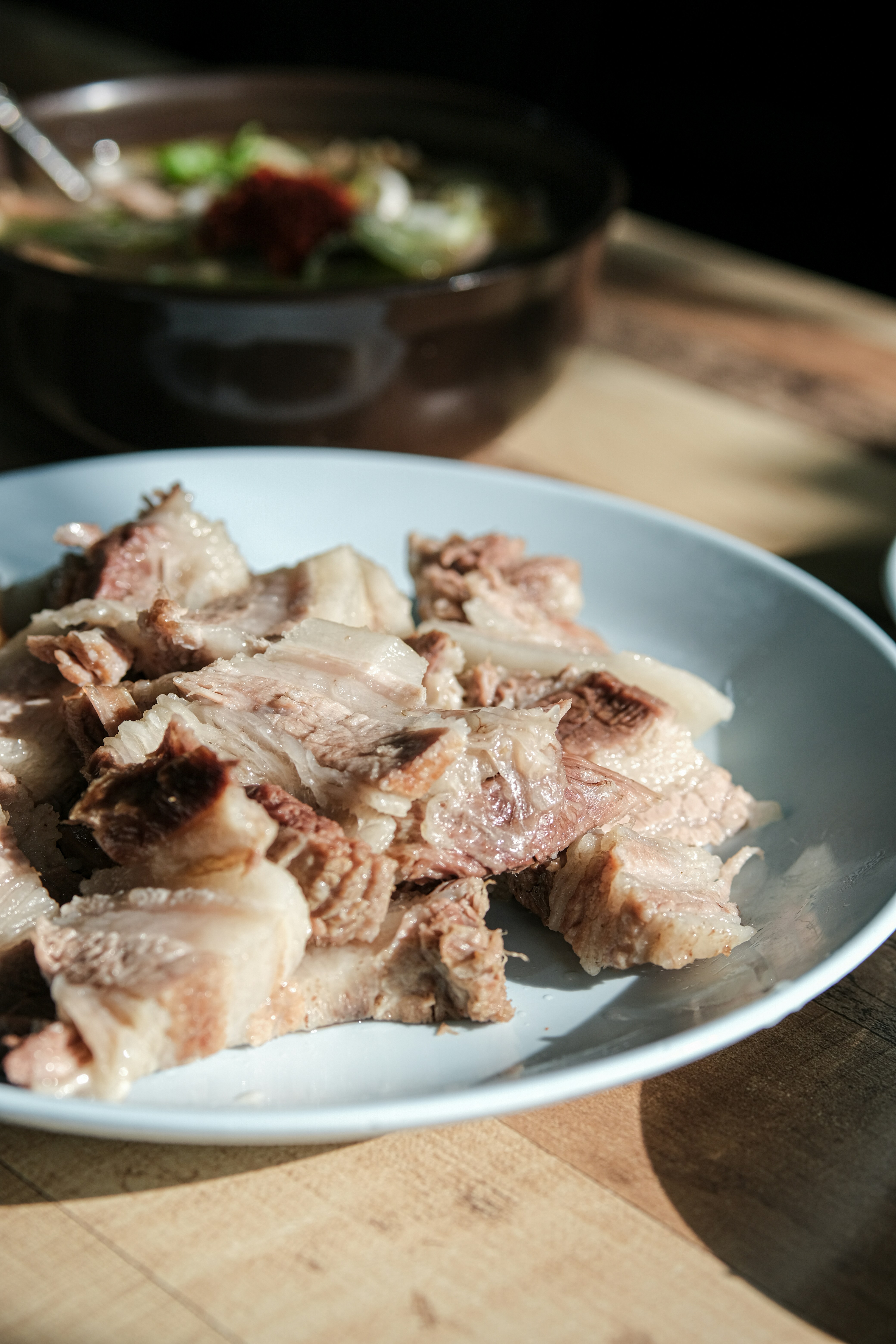 Sunlit Pork Pieces on a Sky-Blue Plate with a Steam-Kissed Bowl in the Background